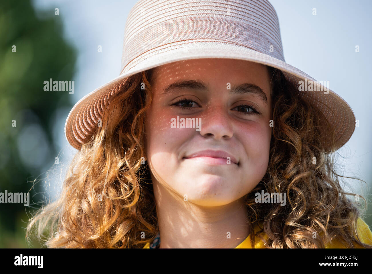 Close-up of a 10-year-old girl with a pamela in the garden of her house ...