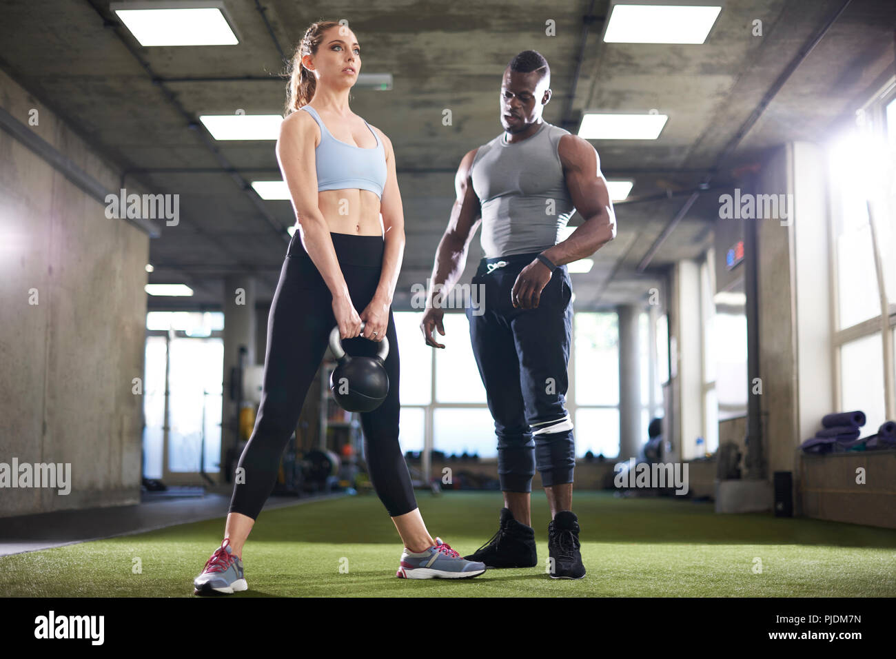 Trainer watching female client exercise with kettlebell in gym Stock ...