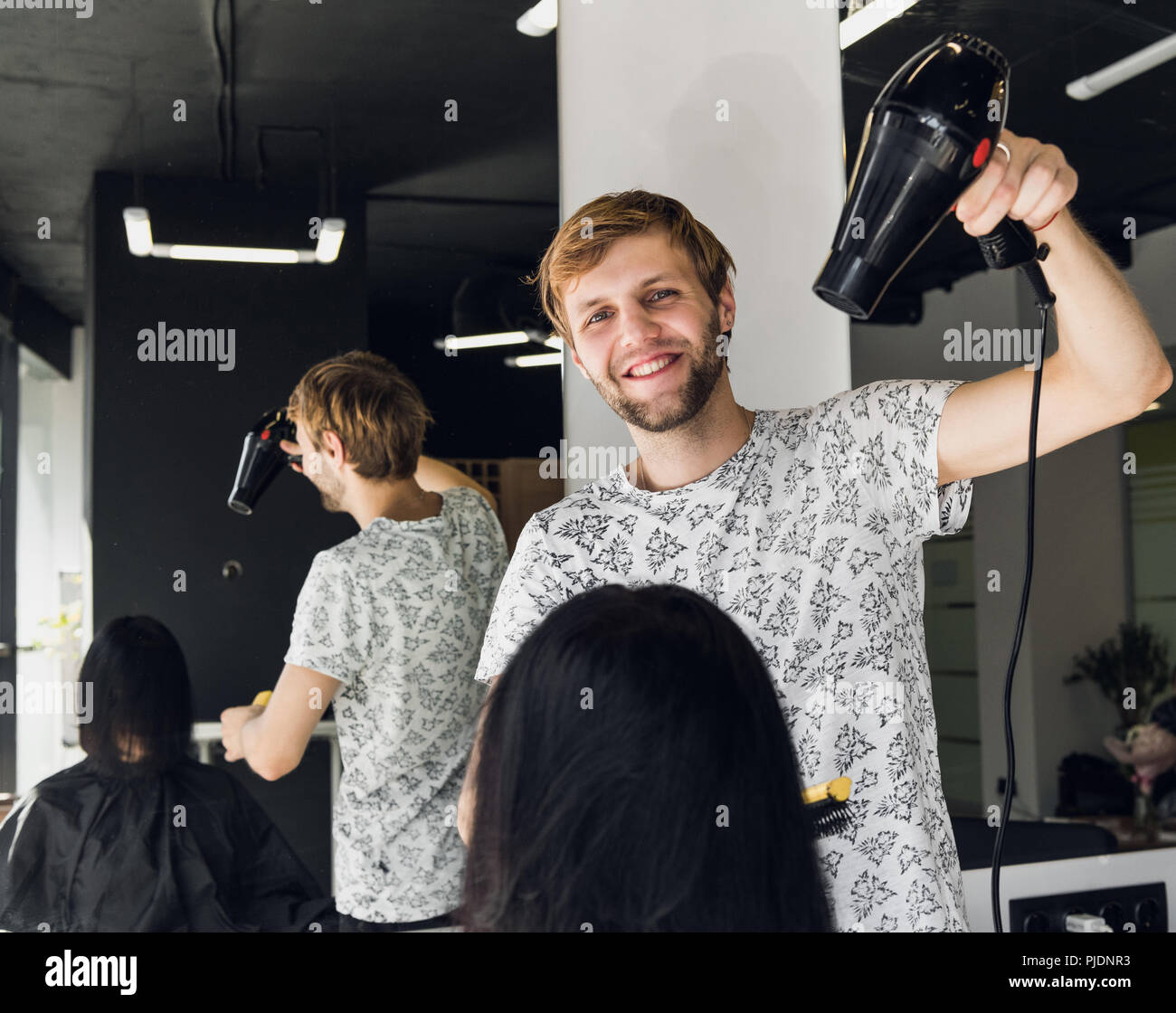 Professional smiling male stylist blow drying woman's hair with a dryer ...