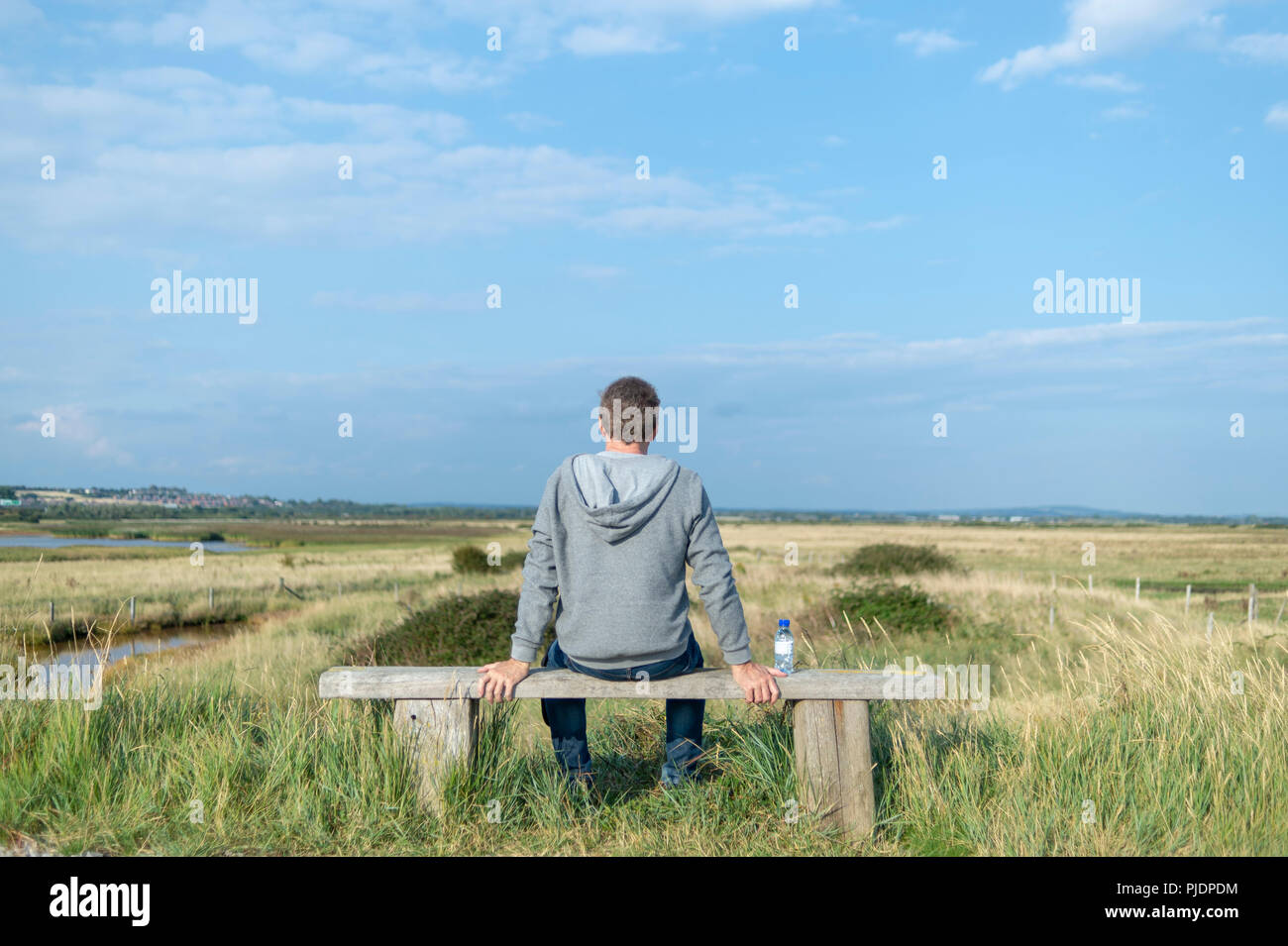 back view of a man sitting on a wooden bench looking at the countryside ...