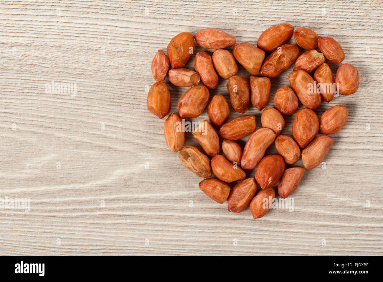 Peanuts in the shape of a heart on grey wooden boards. Top view with ...