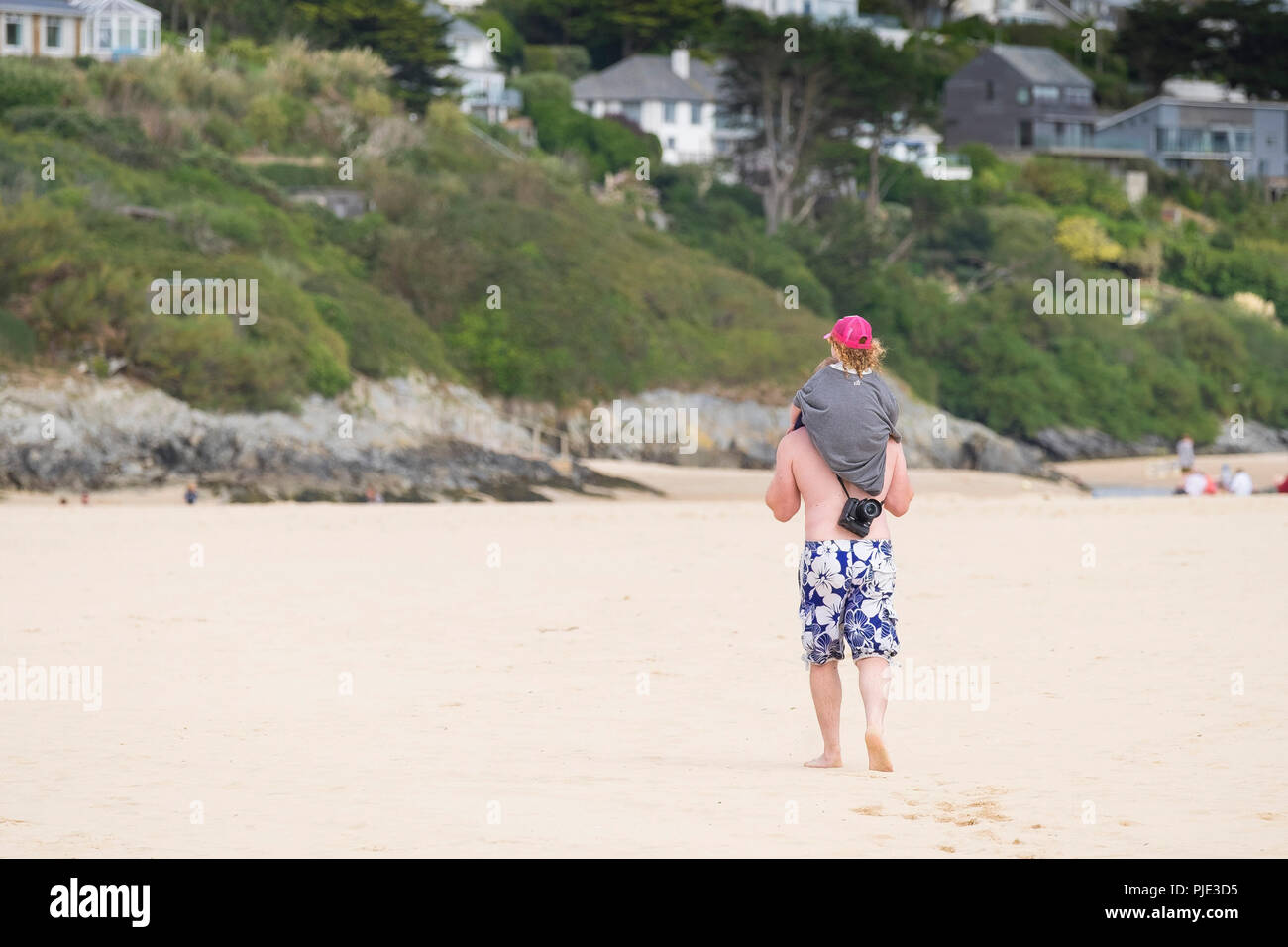 A holidaymaker carrying his child on his shoulders on Crantock Beach in ...