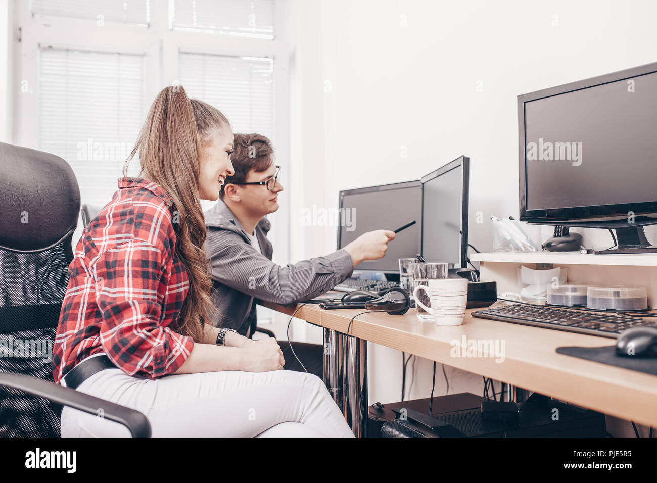 Two smiling colleagues talking together while sitting at a desk in an ...