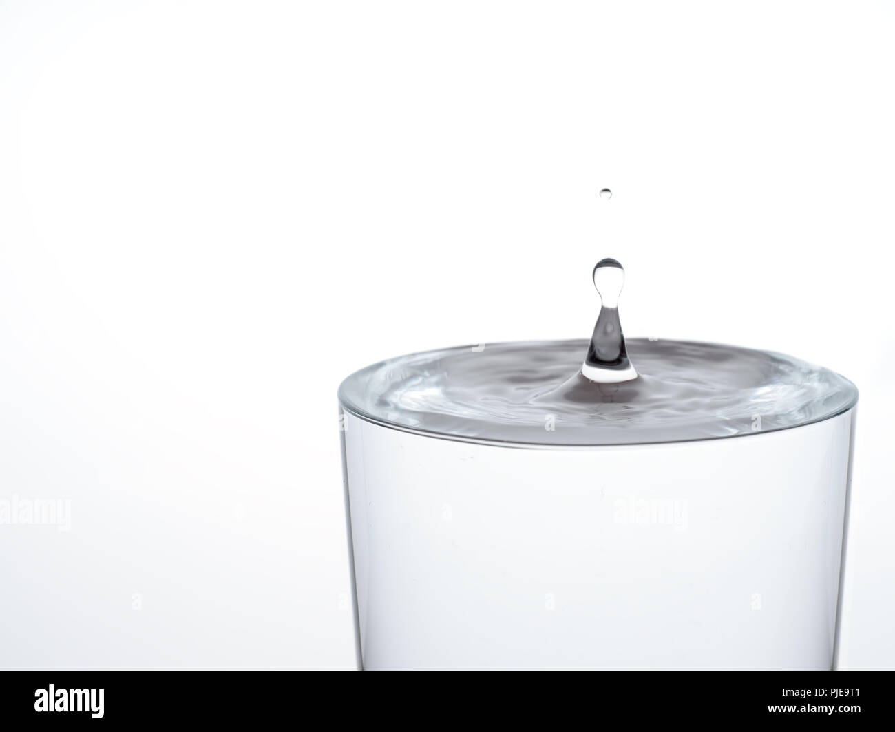 Drop of water, about to make the glass overflow and run over. On white ...