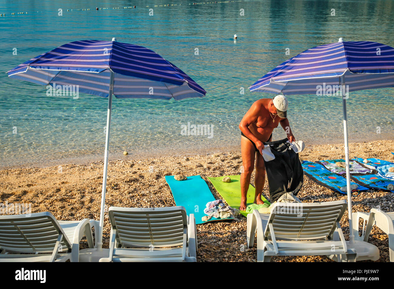 Man prepares for his day of sunbathing and relaxing on the beach by calm waters of the Adriatic ...