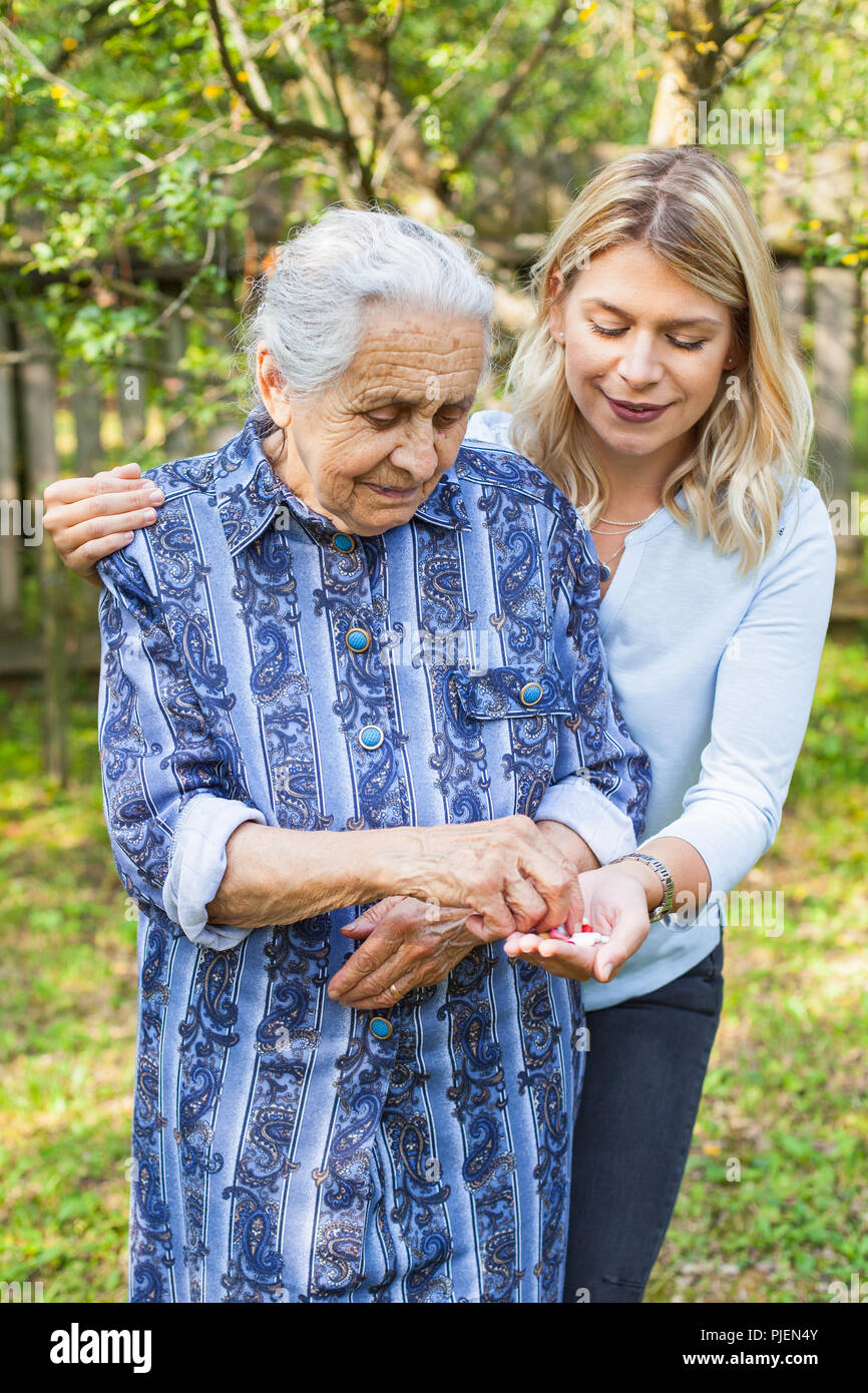 Disabled old lady taking medical pills from friendly carer's hand ...