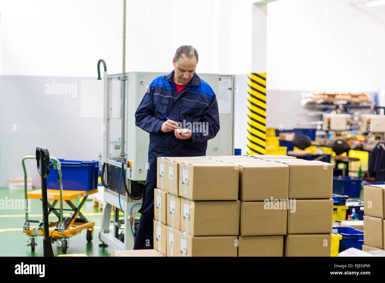 Factory worker taking notes while checking boxes in factory warehouse ...