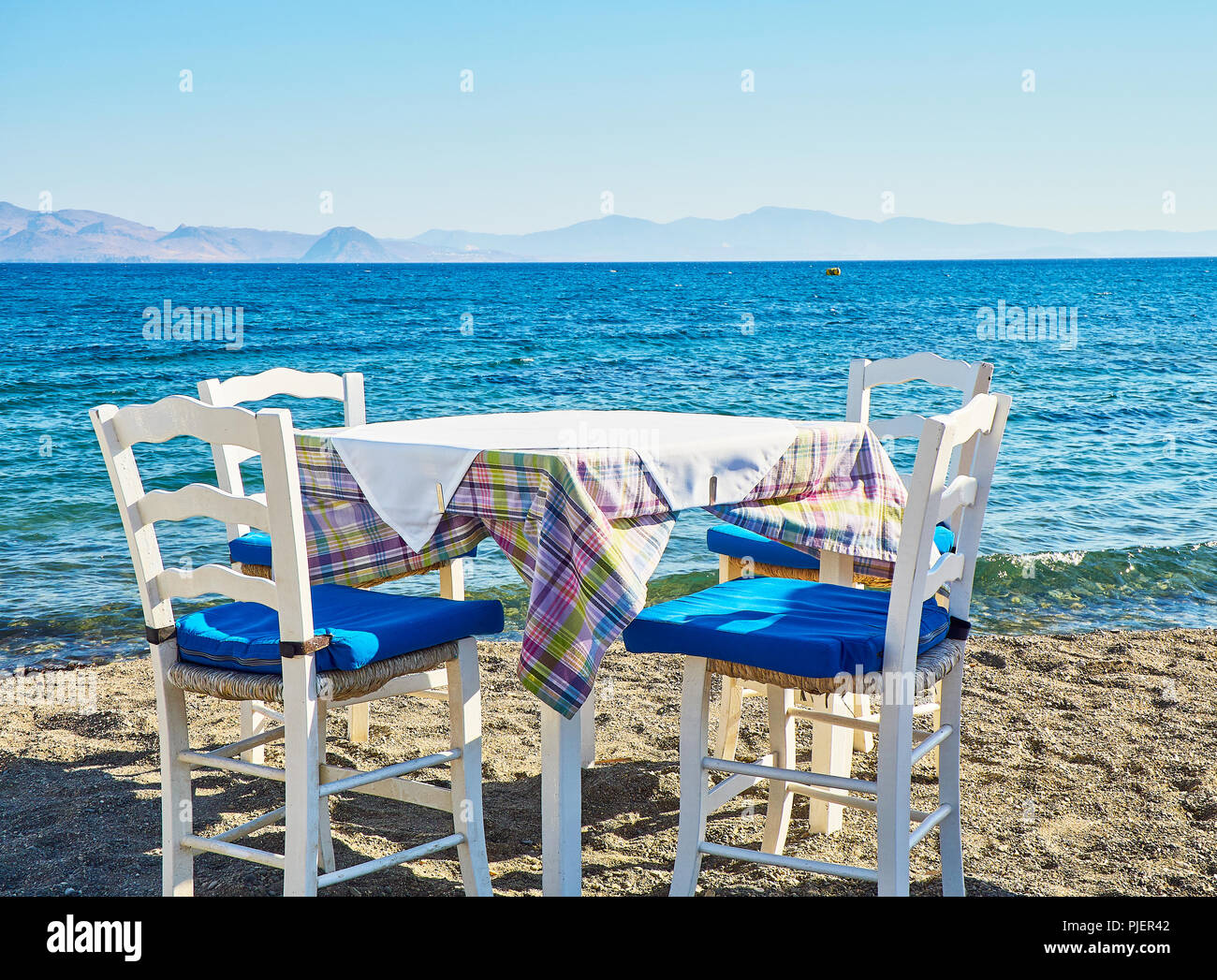 A table with chairs of a greek tavern near the sea in a beach of Kos ...