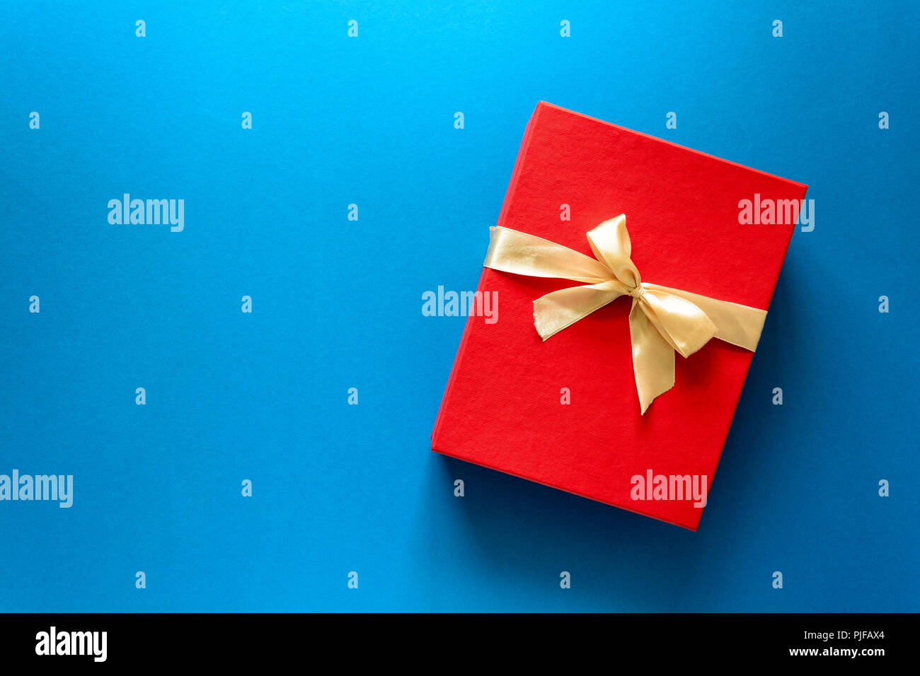Top view on red Christmas gift box decorated with ribbon on blue paper ...