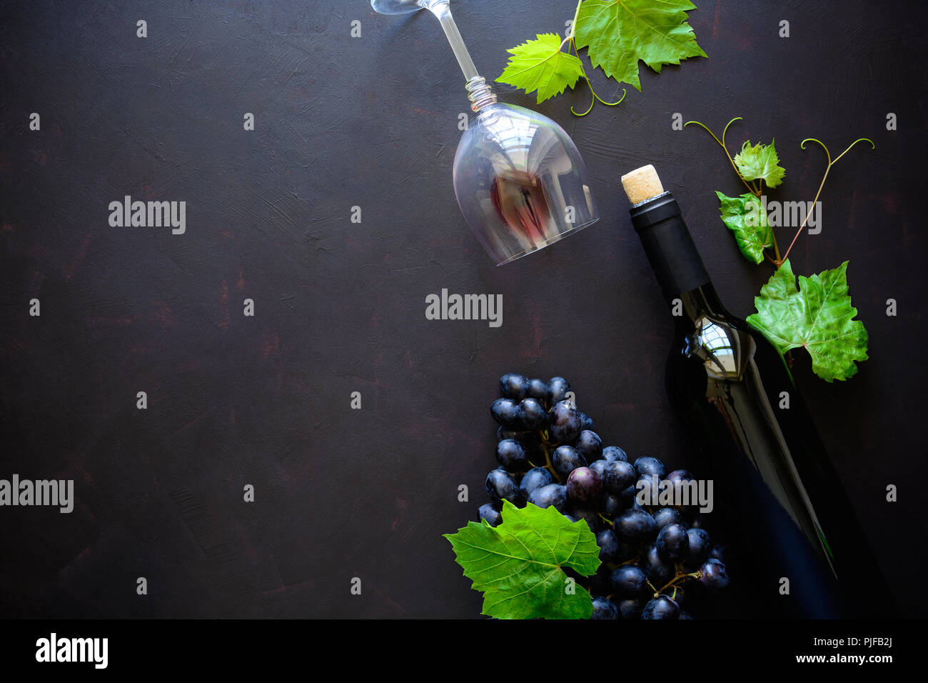 Two wineglasses with red wine, bottle and grape leaves lying on dark ...