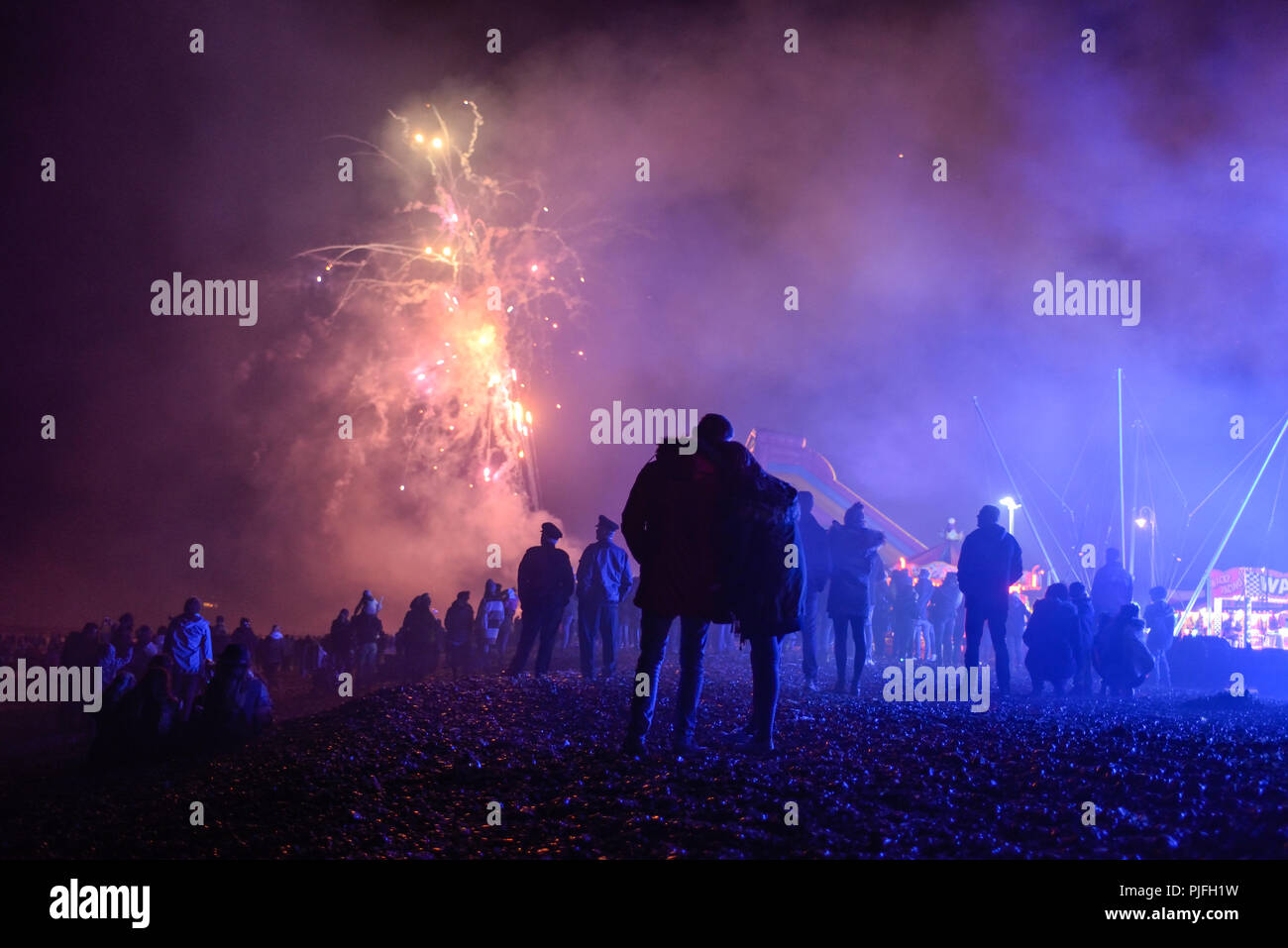 A couple hug on the beach as they watch fireworks explode above their ...