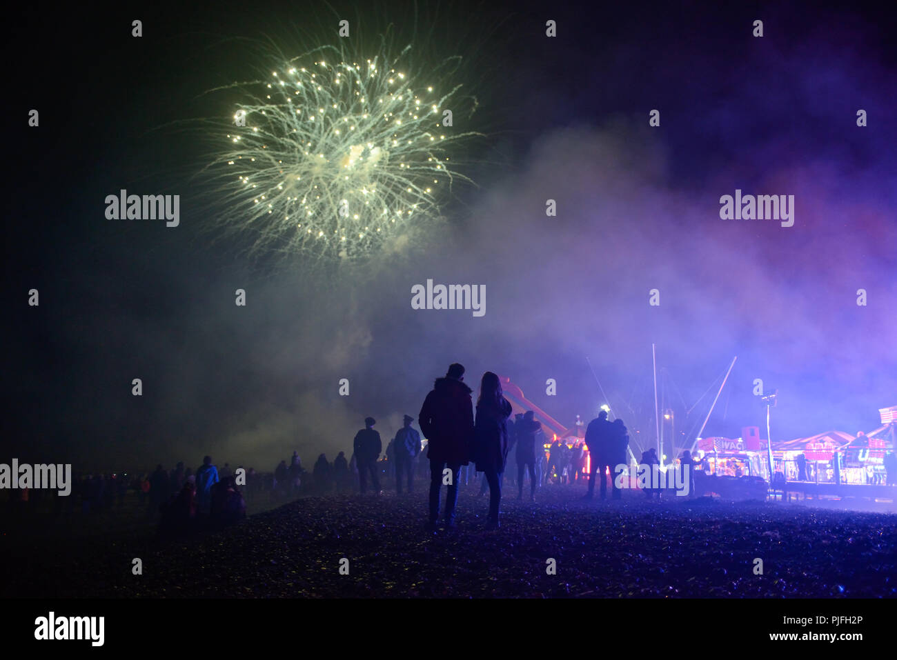 A couple hold hands on the beach as they watch fireworks explode above ...