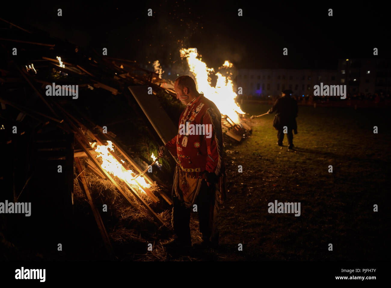 A man lights a large bonfire with a flaming torch during the Bonfire ...
