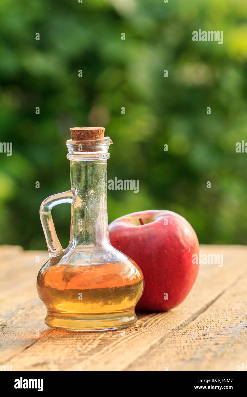 Apple vinegar in glass bottle with cork and fresh red apple on wooden ...