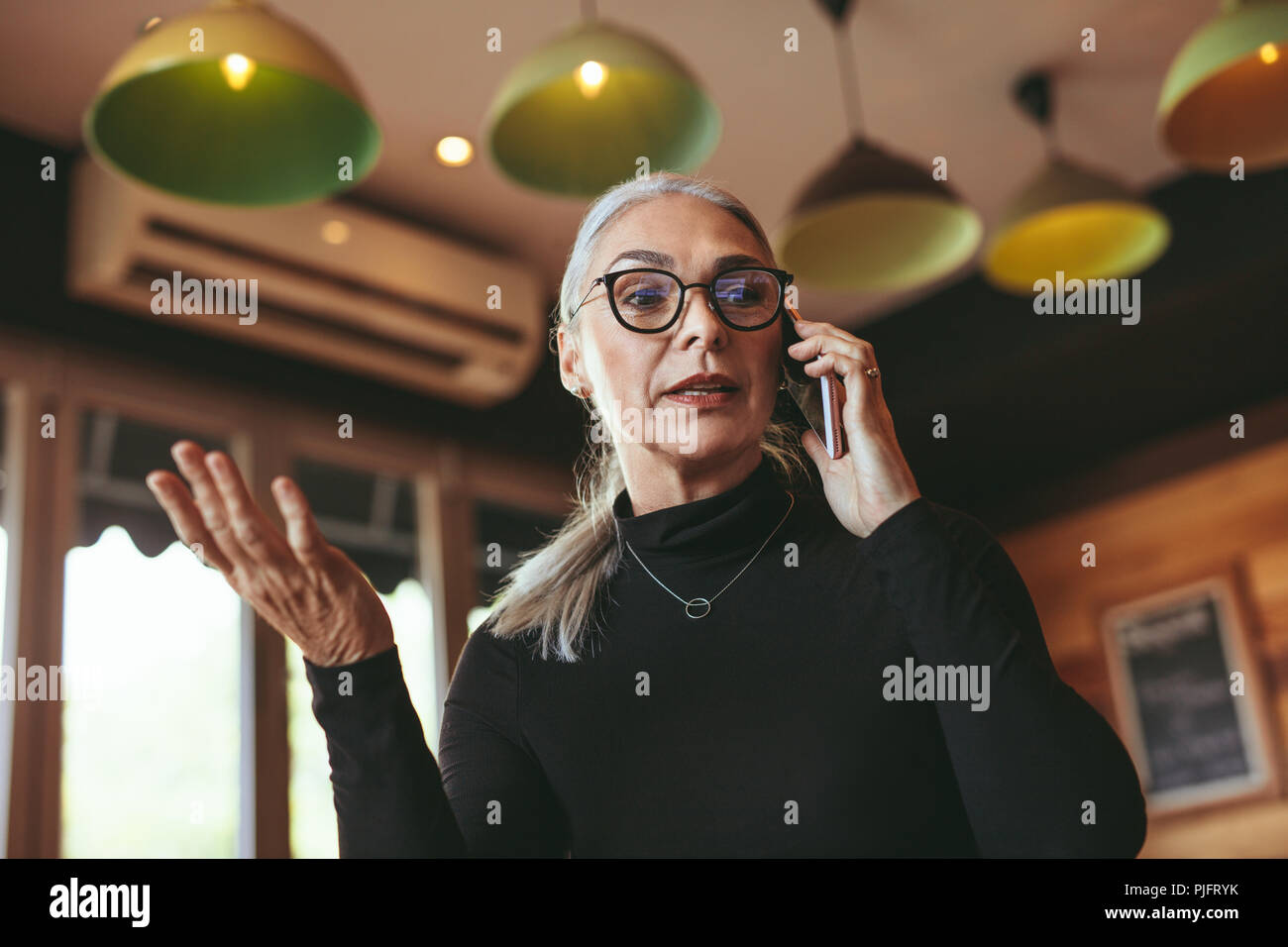 Senior woman calling with cell phone while sitting alone in coffee shop ...