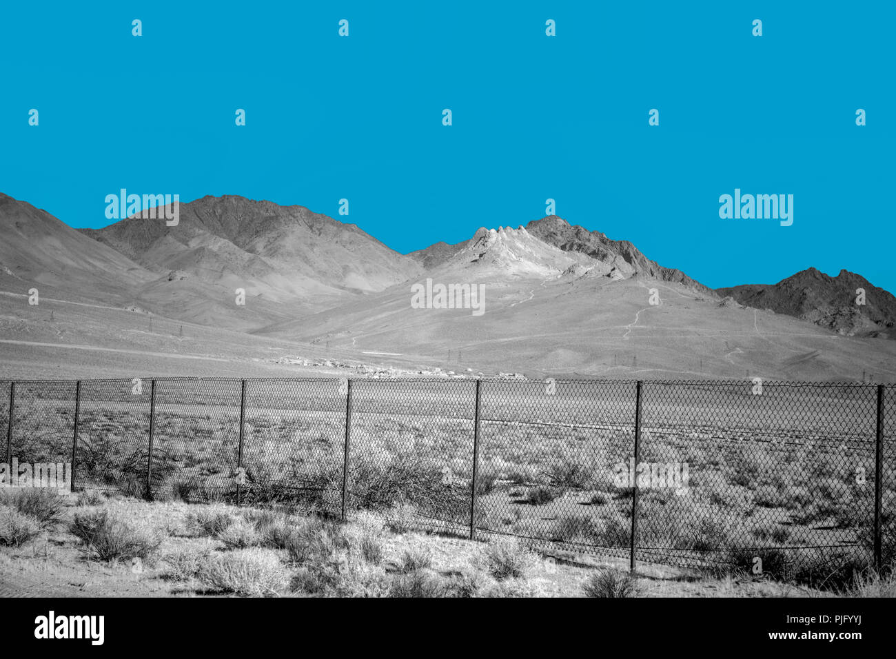 A fence dividing the desert landscape with cold barren mountains under ...