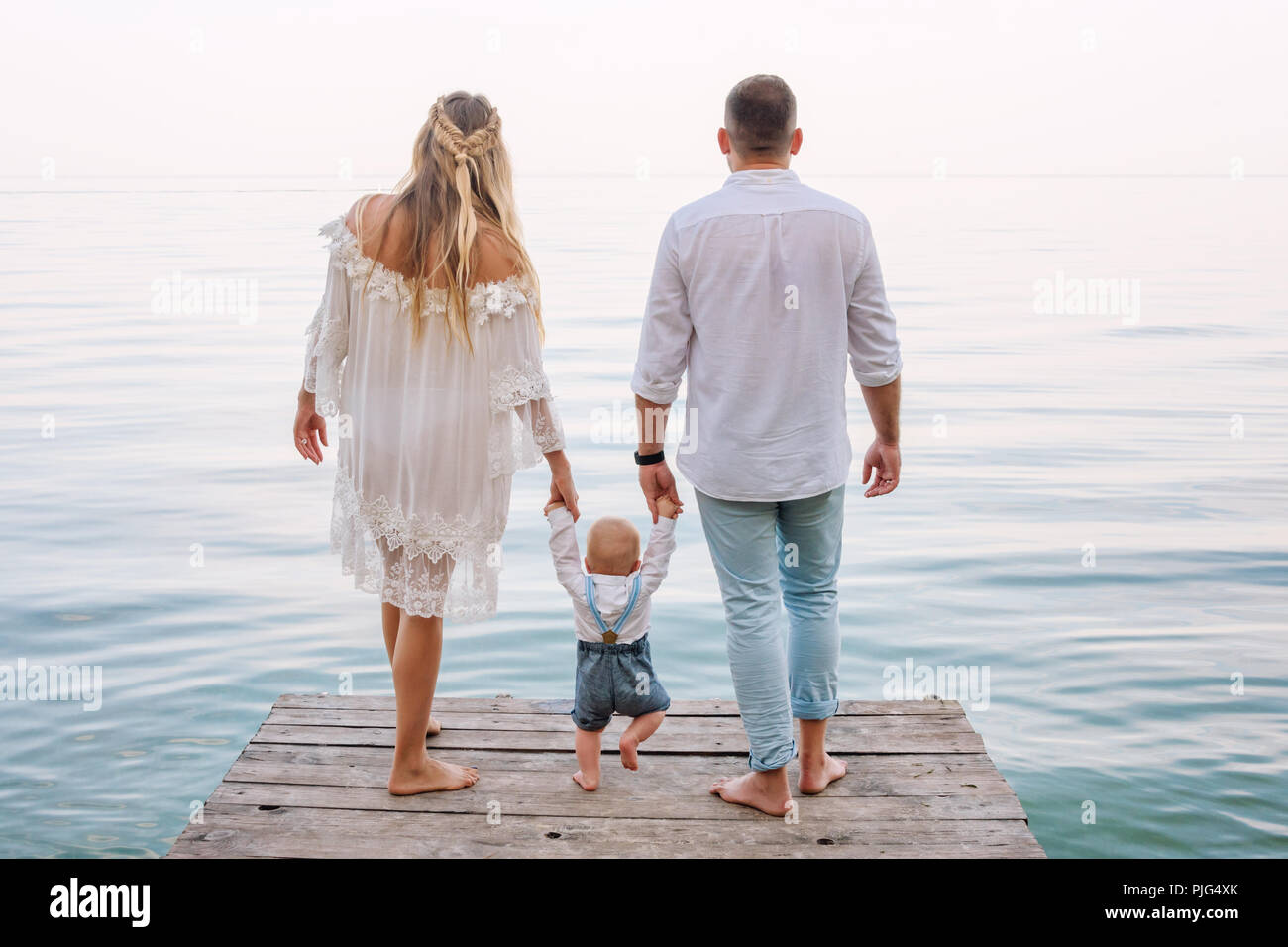 Happy family on pier. Back view. Man and woman holding their toddler ...