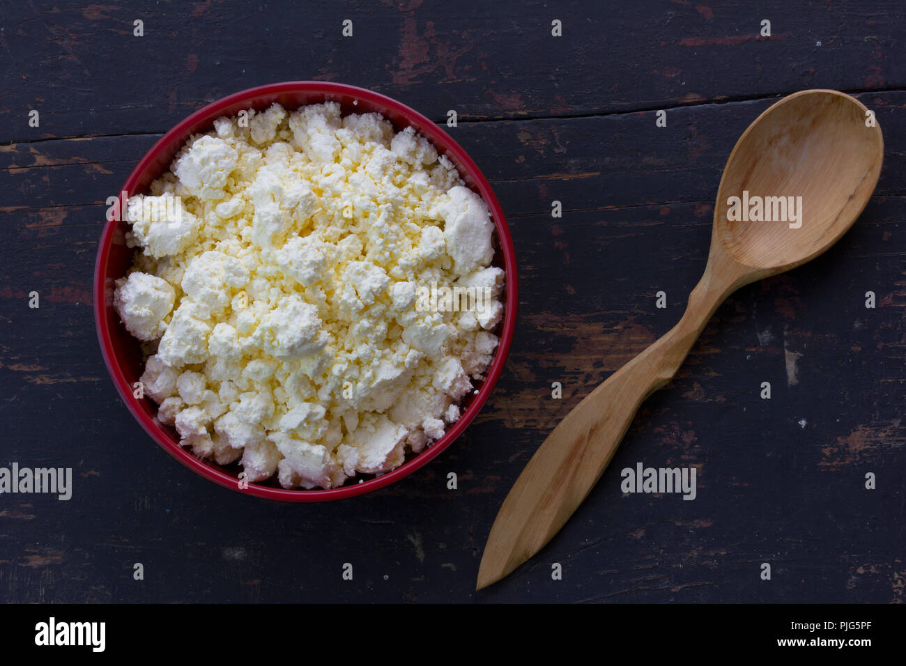 red plate with white milky curd and juniper wooden spoon on an old ...