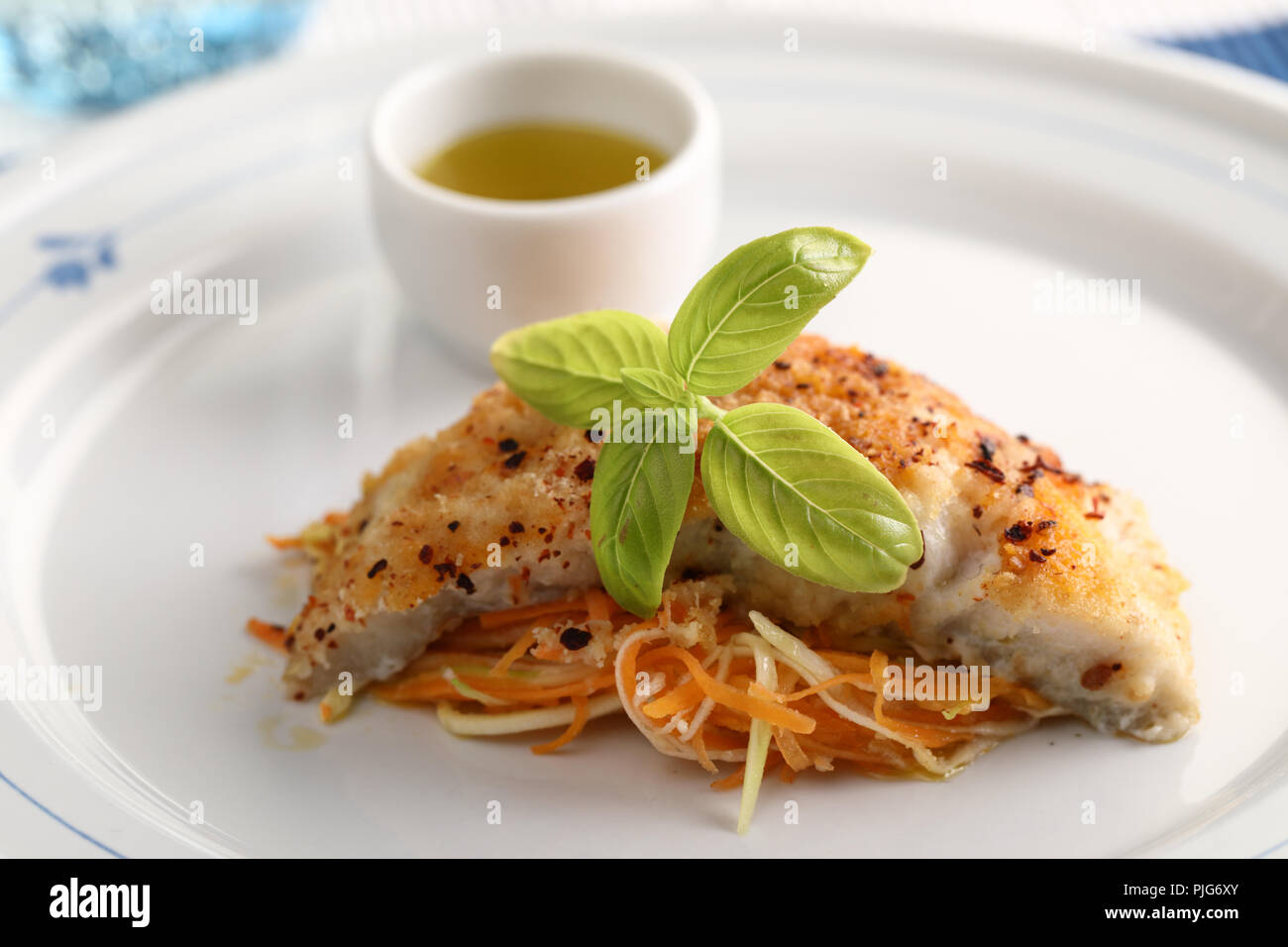 Baked breaded cod fish on vegetable bed topped with basil leaf Stock ...
