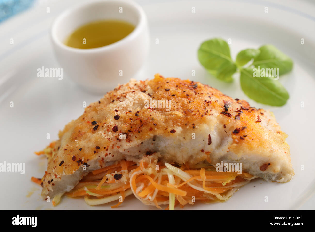 Baked breaded cod fish on vegetable bed topped with basil leaf Stock ...