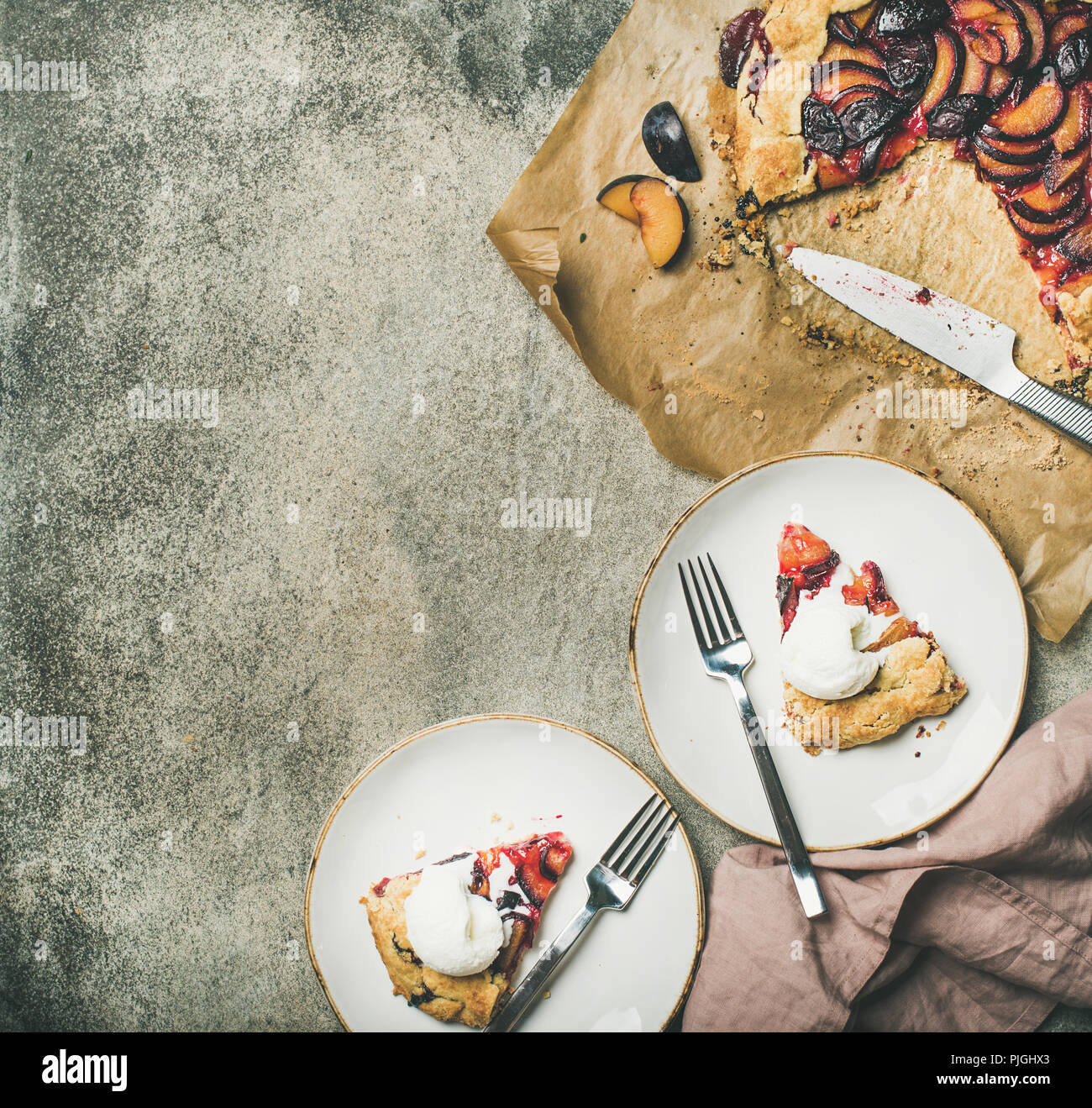 Flat-lay of plum galetta sweet cake in white plates over grey concrete ...