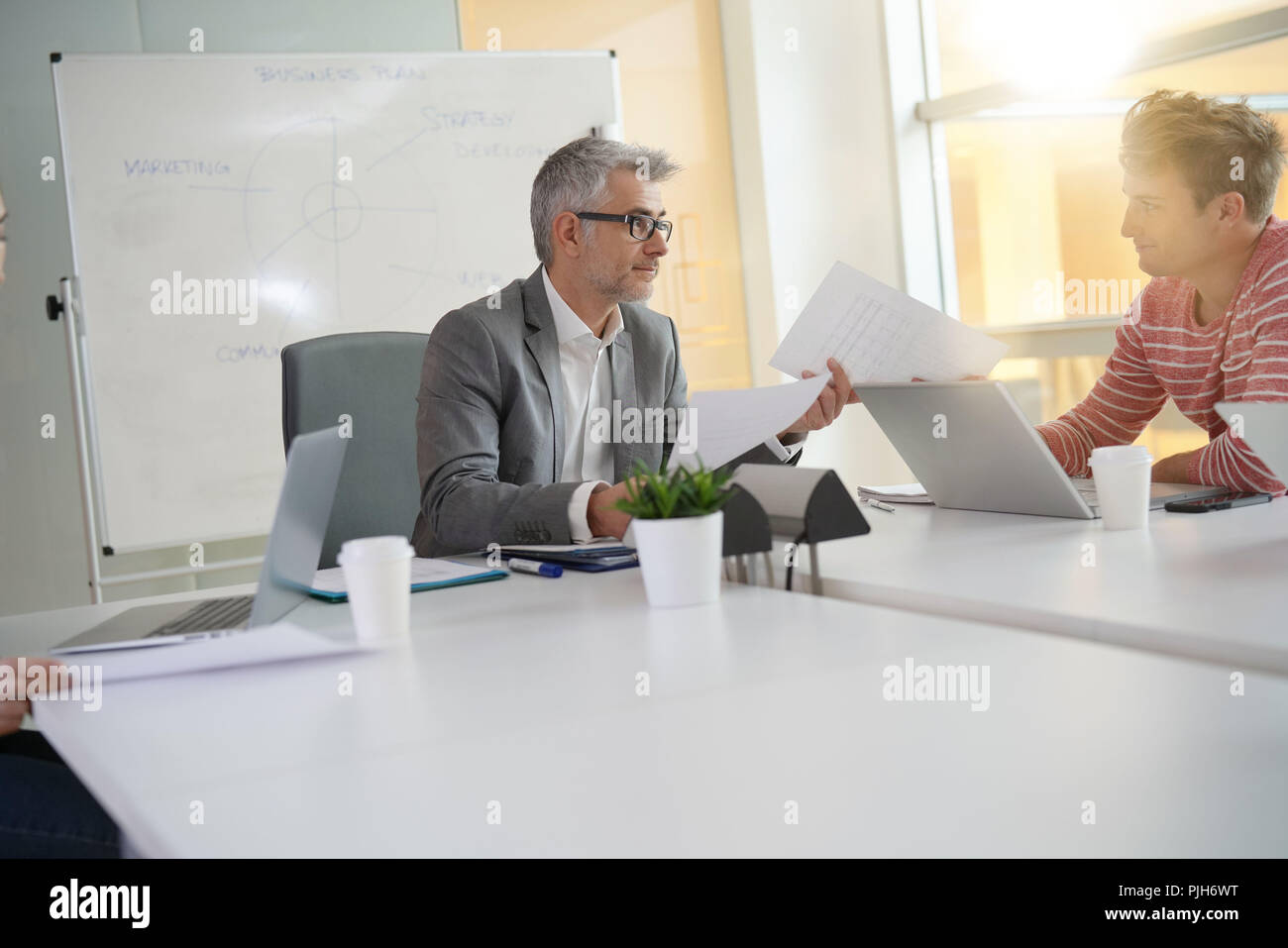 Teacher giving copies to students around table Stock Photo - Alamy