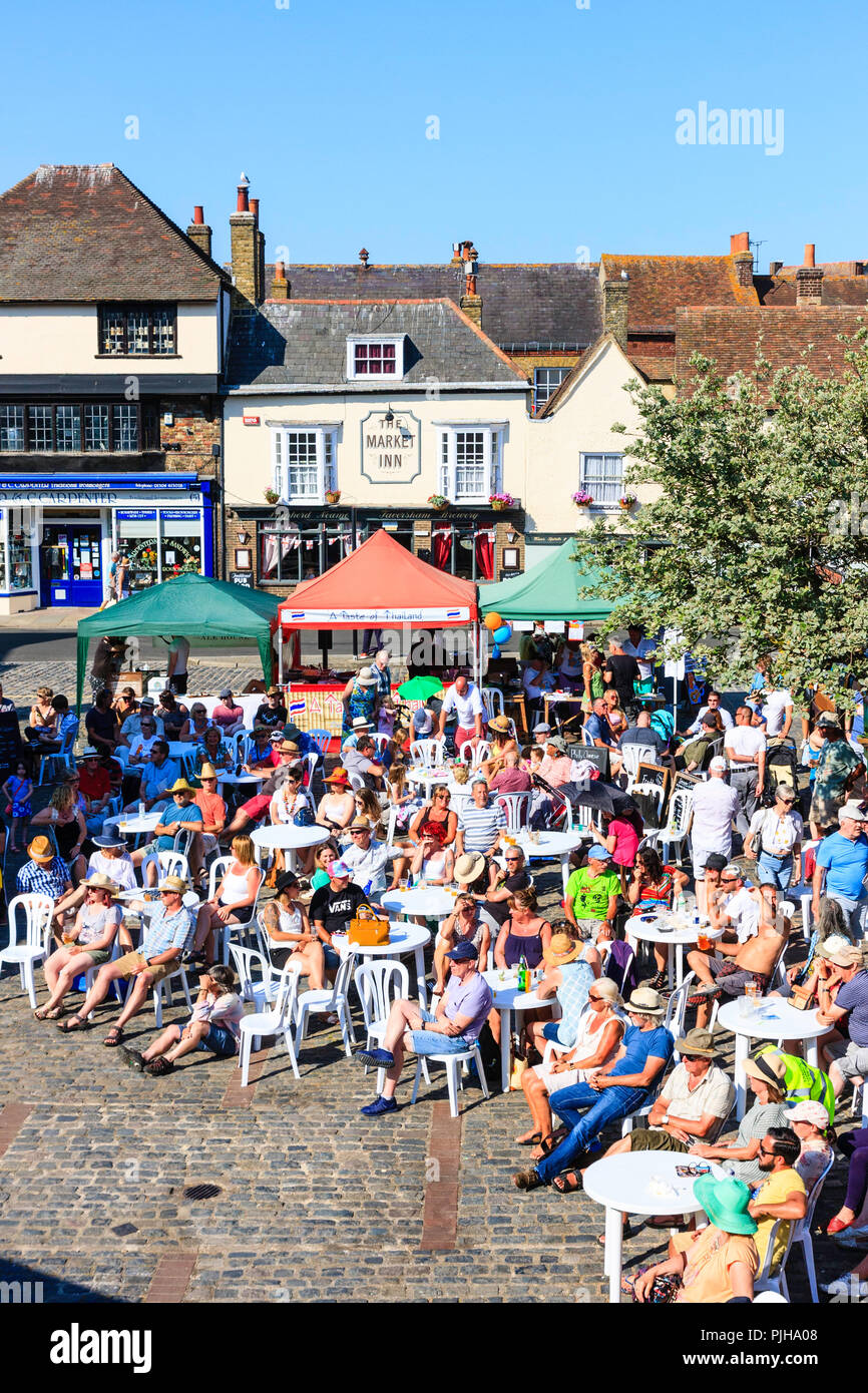Crowd of people, audience, sitting at tables in cobbled town square in ...