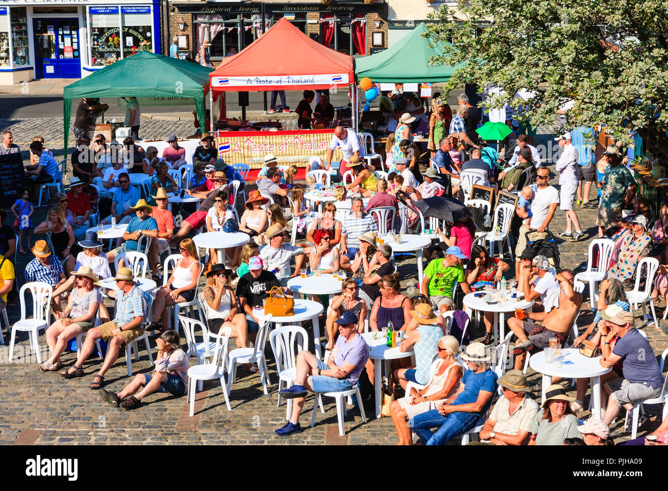 Crowd of people, audience, sitting at tables in cobbled town square in ...