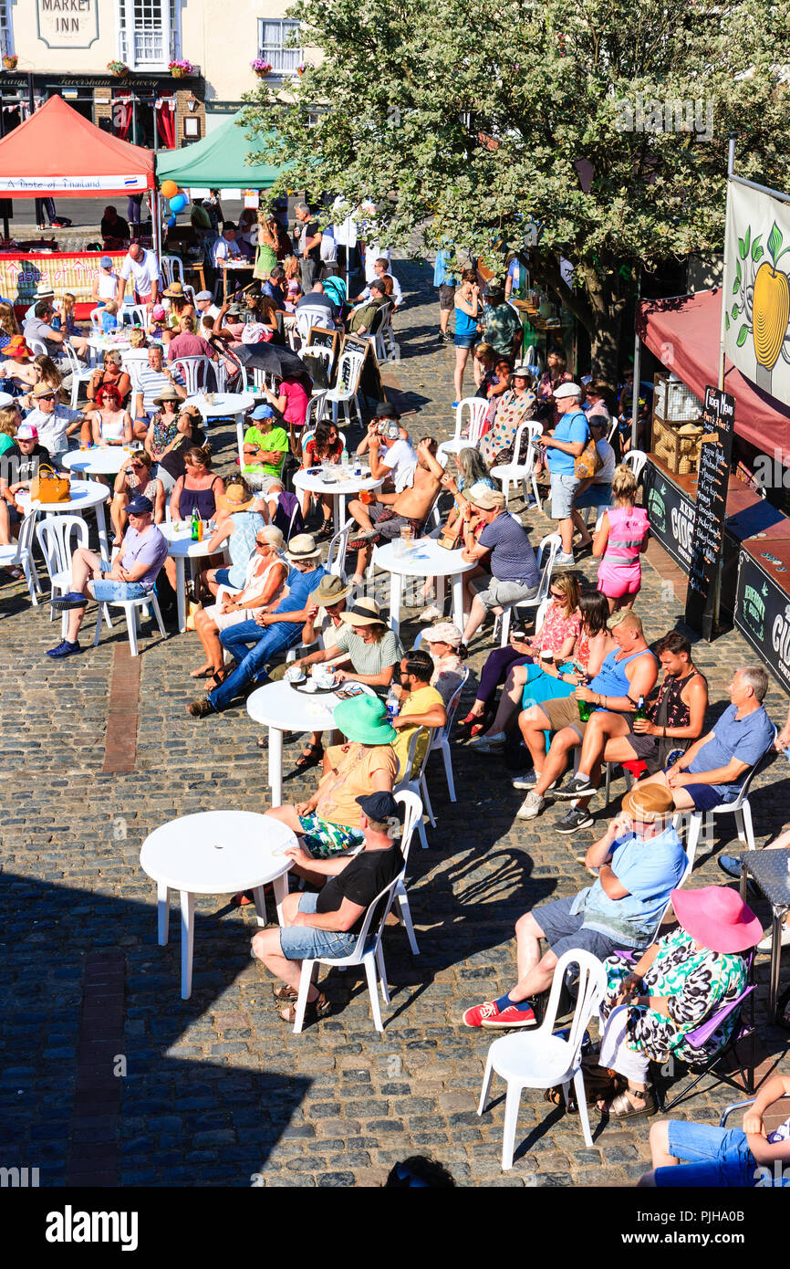 Crowd of people, audience, sitting at tables in cobbled town square in ...