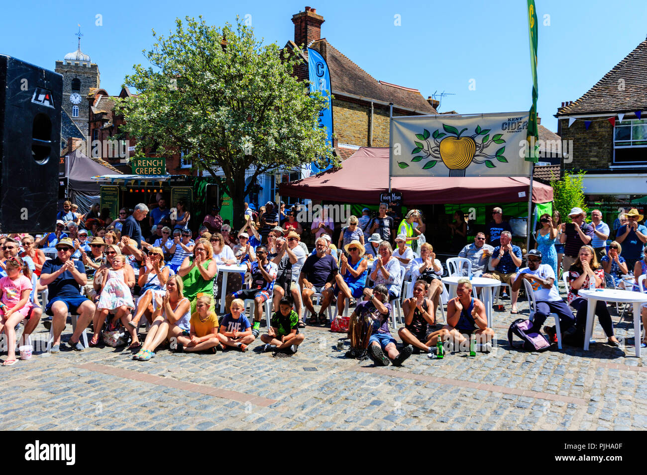 Crowd of people, audience, sitting at tables in cobbled town square in ...