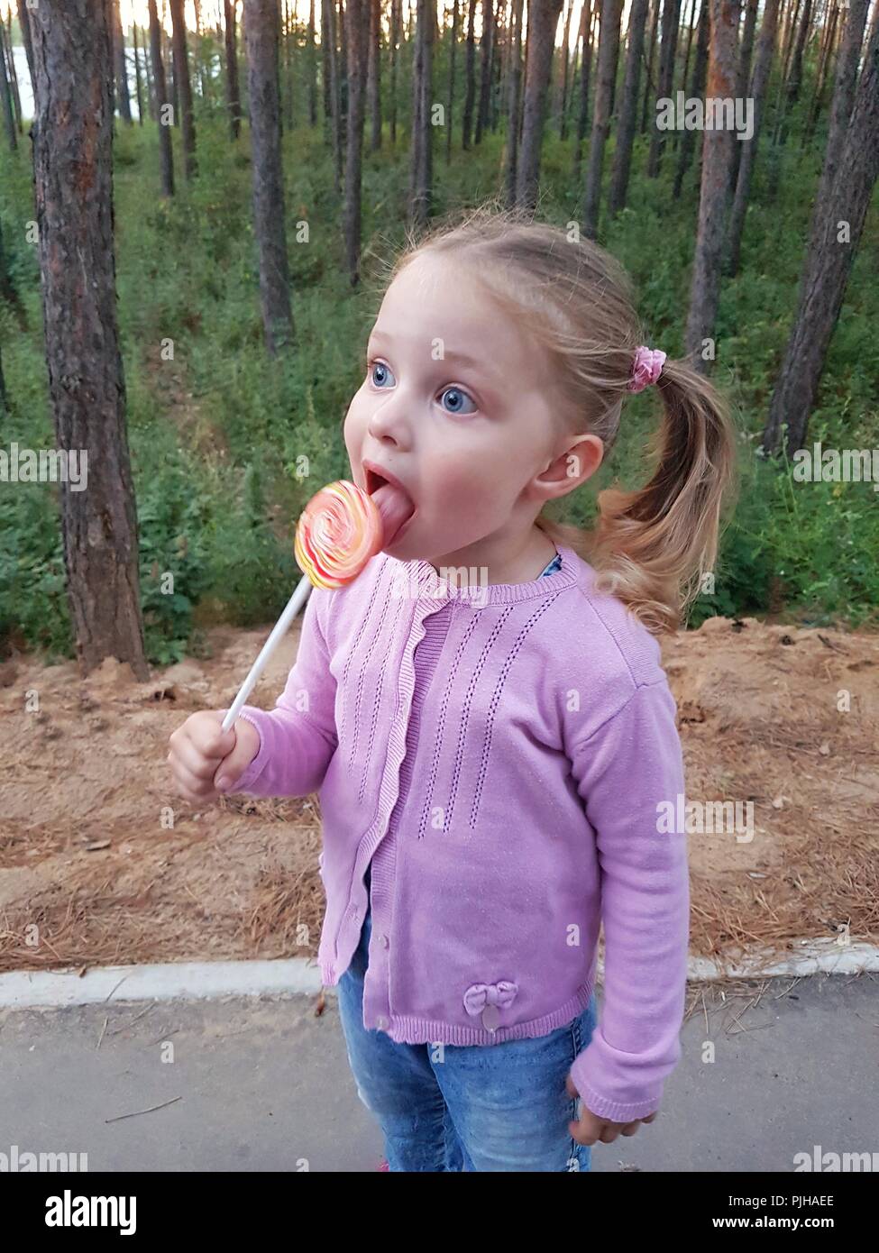 Funny child with candy lollipop, happy little girl eating big sugar ...