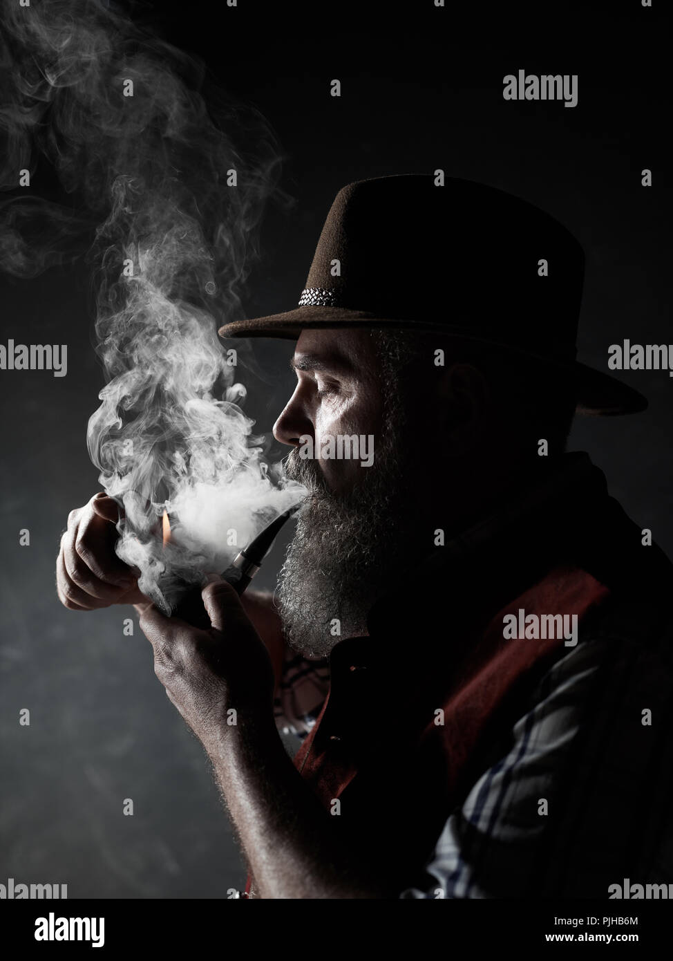dramatic portrait of senior man in hat smoking tobacco pipe. Profile ...