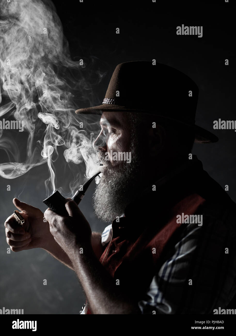 dramatic portrait of senior man in hat smoking tobacco pipe. Profile ...