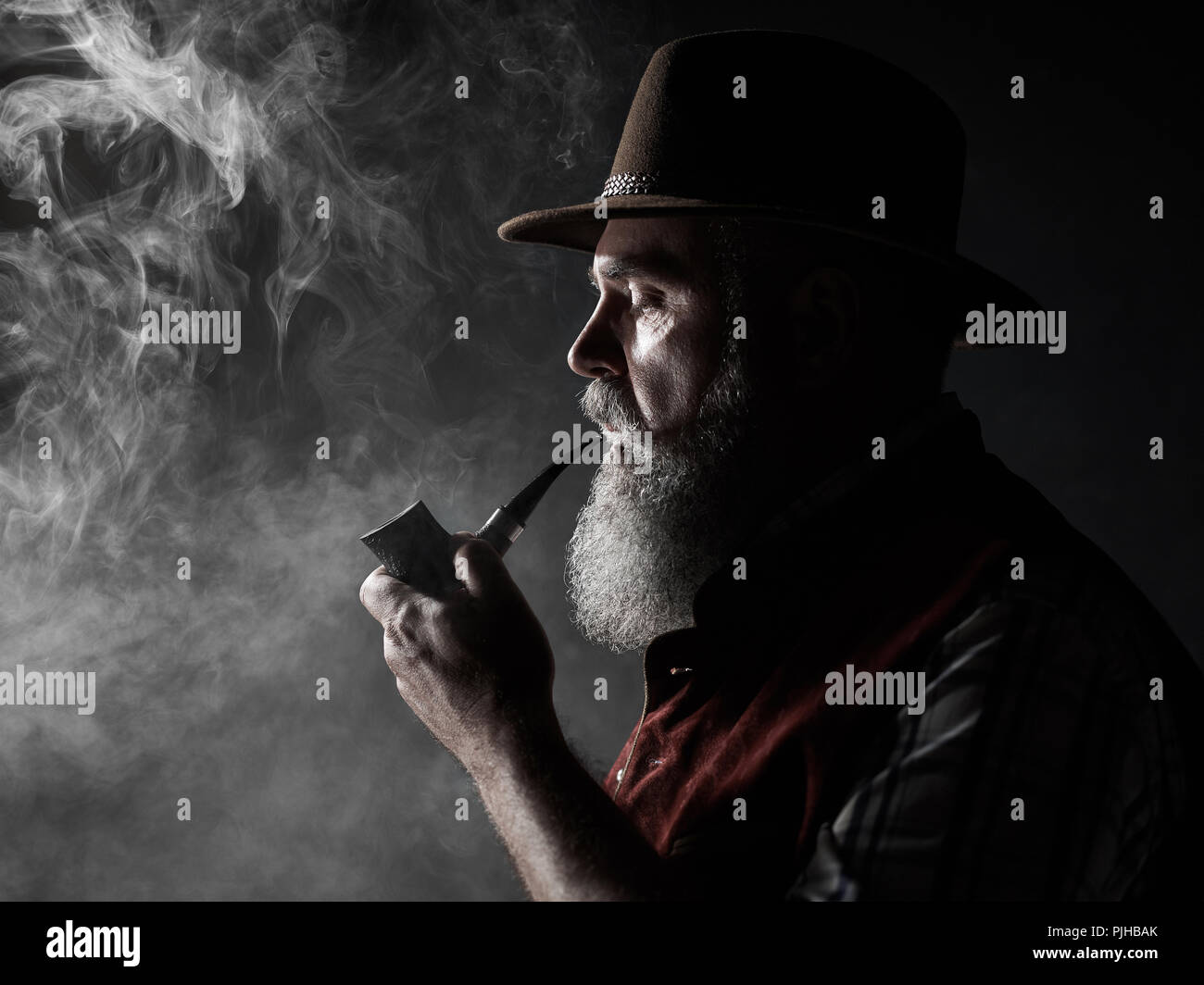 dramatic portrait of senior man in hat smoking tobacco pipe. Profile ...