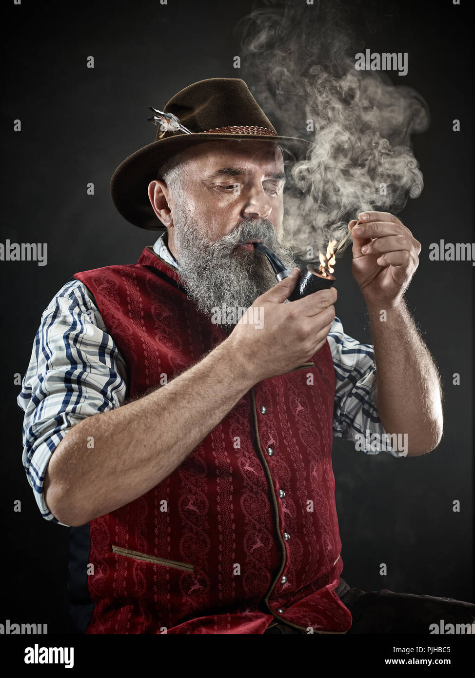 dramatic portrait of gray bearded senior man in hat smoking tobacco ...