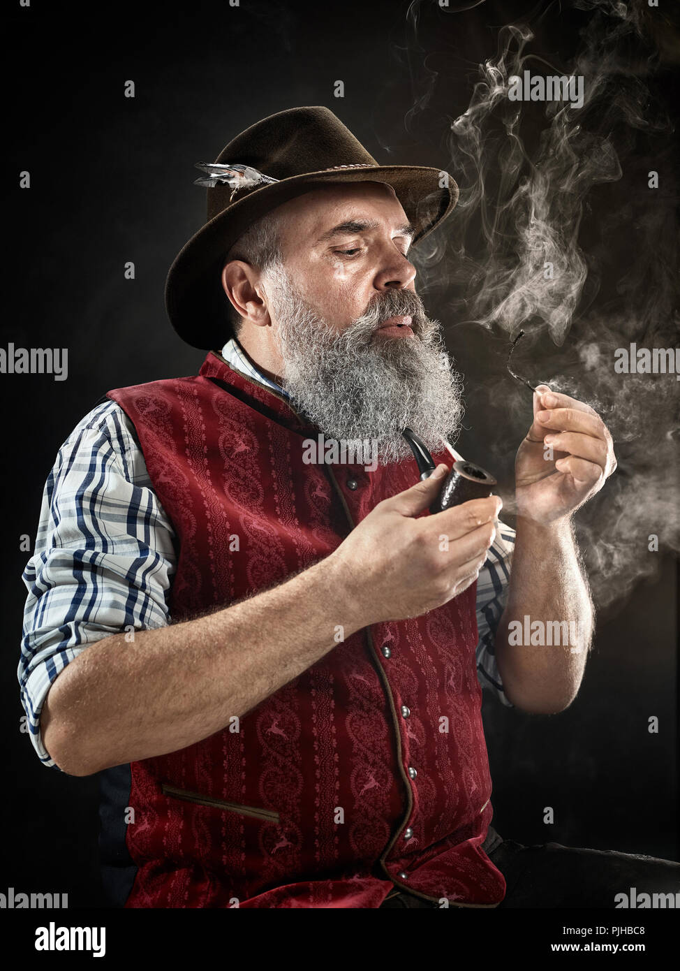 dramatic portrait of gray bearded senior man in hat smoking tobacco ...