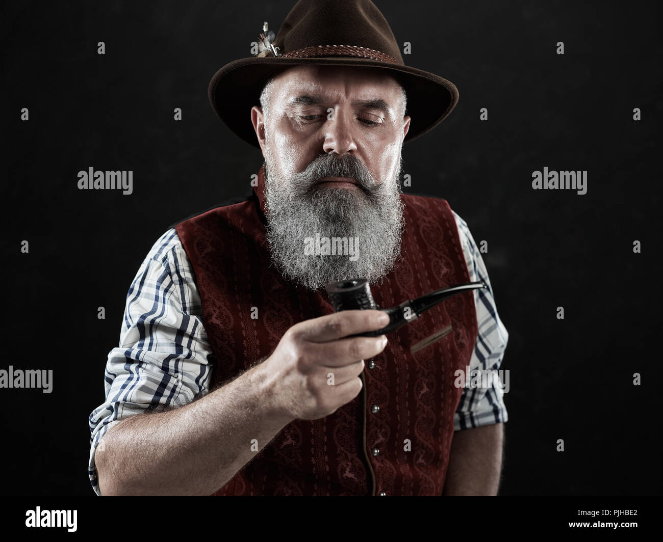 dramatic portrait of gray bearded senior man in hat smoking tobacco ...