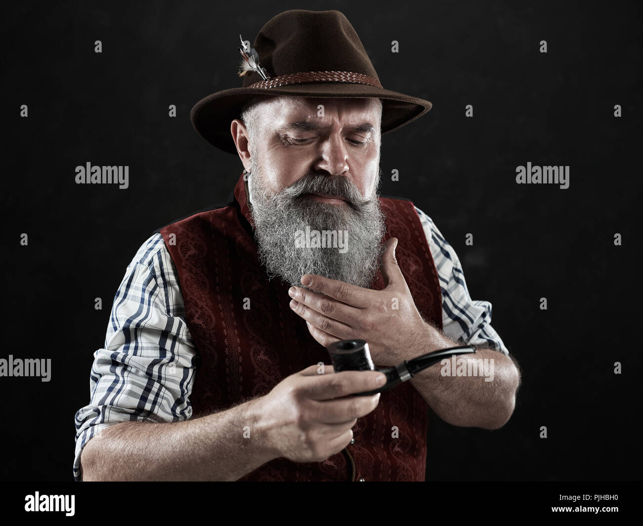 dramatic portrait of gray bearded senior man in hat smoking tobacco ...