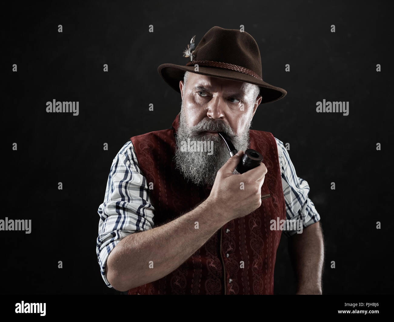 dramatic portrait of gray bearded senior man in hat smoking tobacco ...