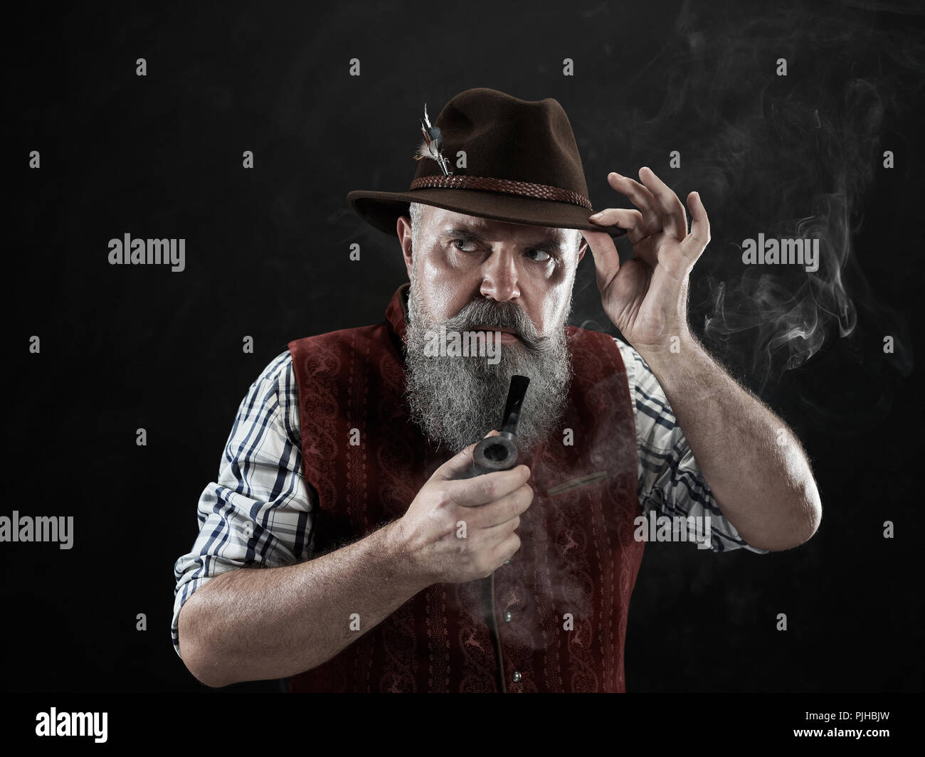 dramatic portrait of gray bearded senior man in hat smoking tobacco ...