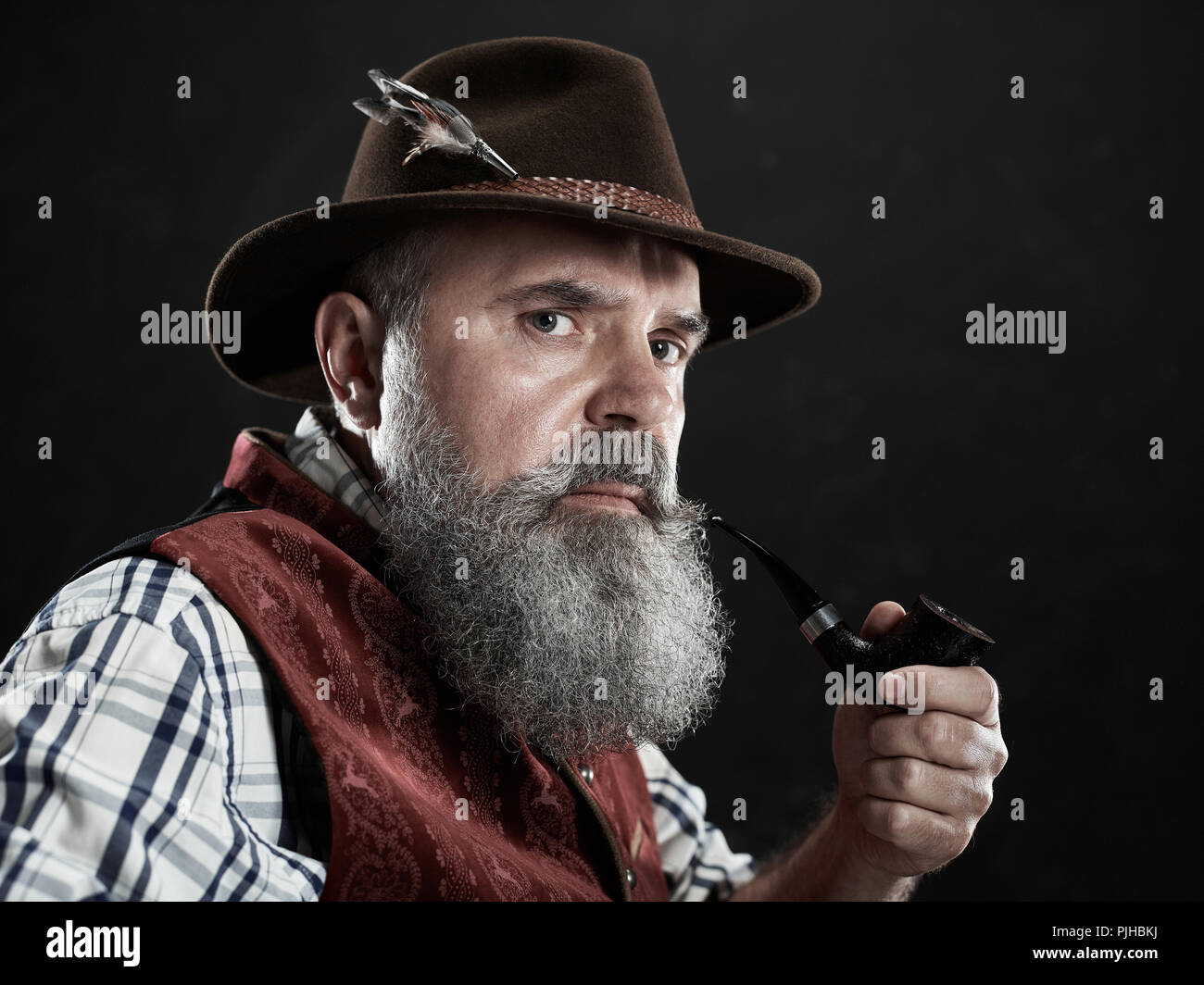 dramatic portrait of gray bearded senior man in hat smoking tobacco ...