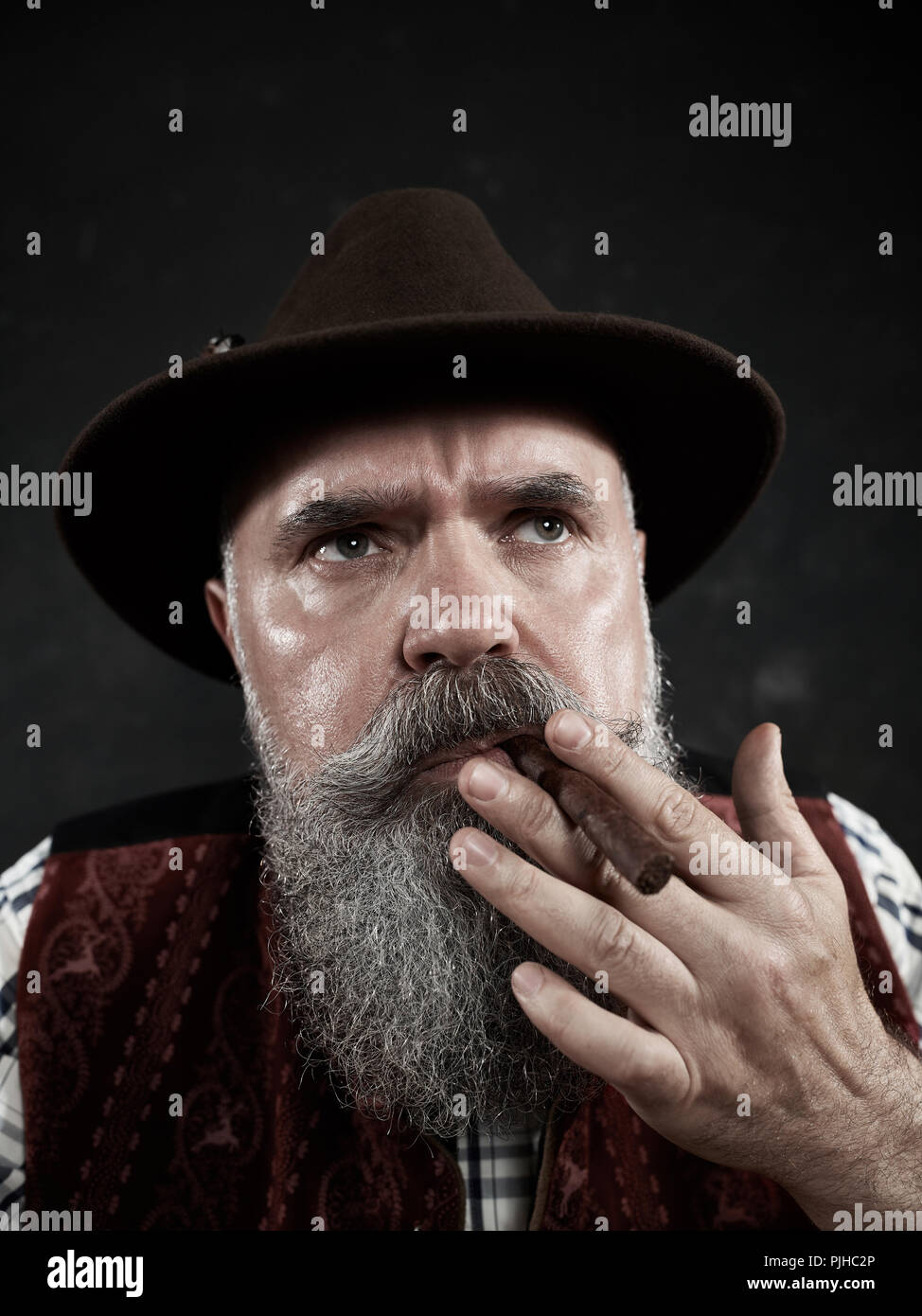 dramatic portrait of gray bearded senior man in hat smoking tobacco ...