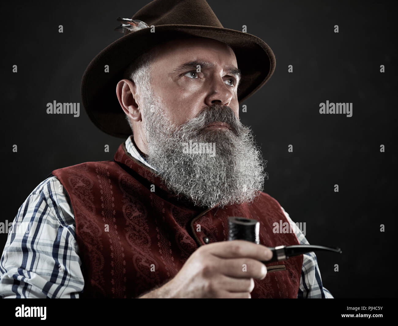 dramatic portrait of gray bearded senior man in hat smoking tobacco ...