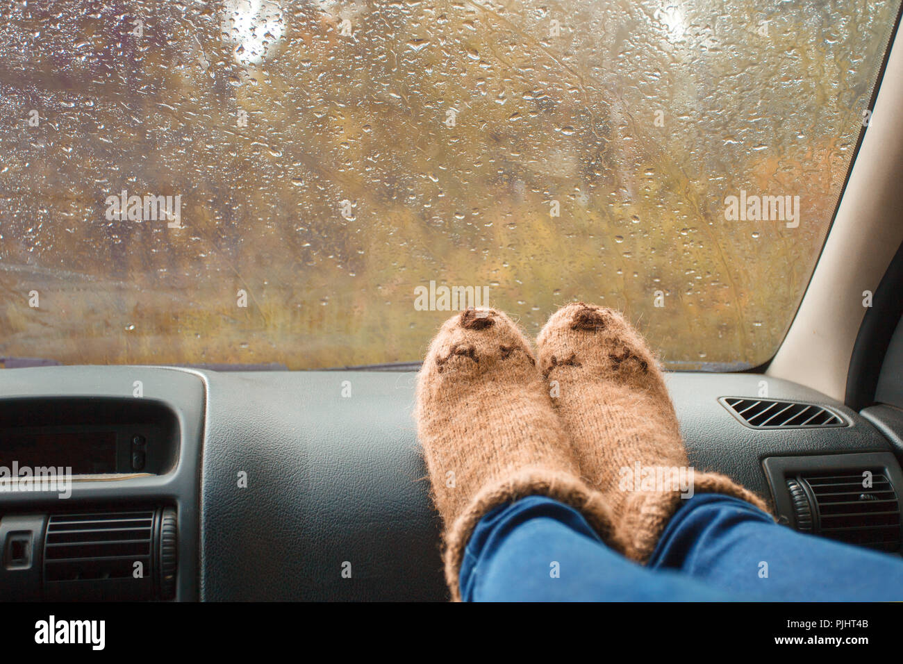 Woman legs in warm cute socks on car dashboard. Drinking warm tee on ...