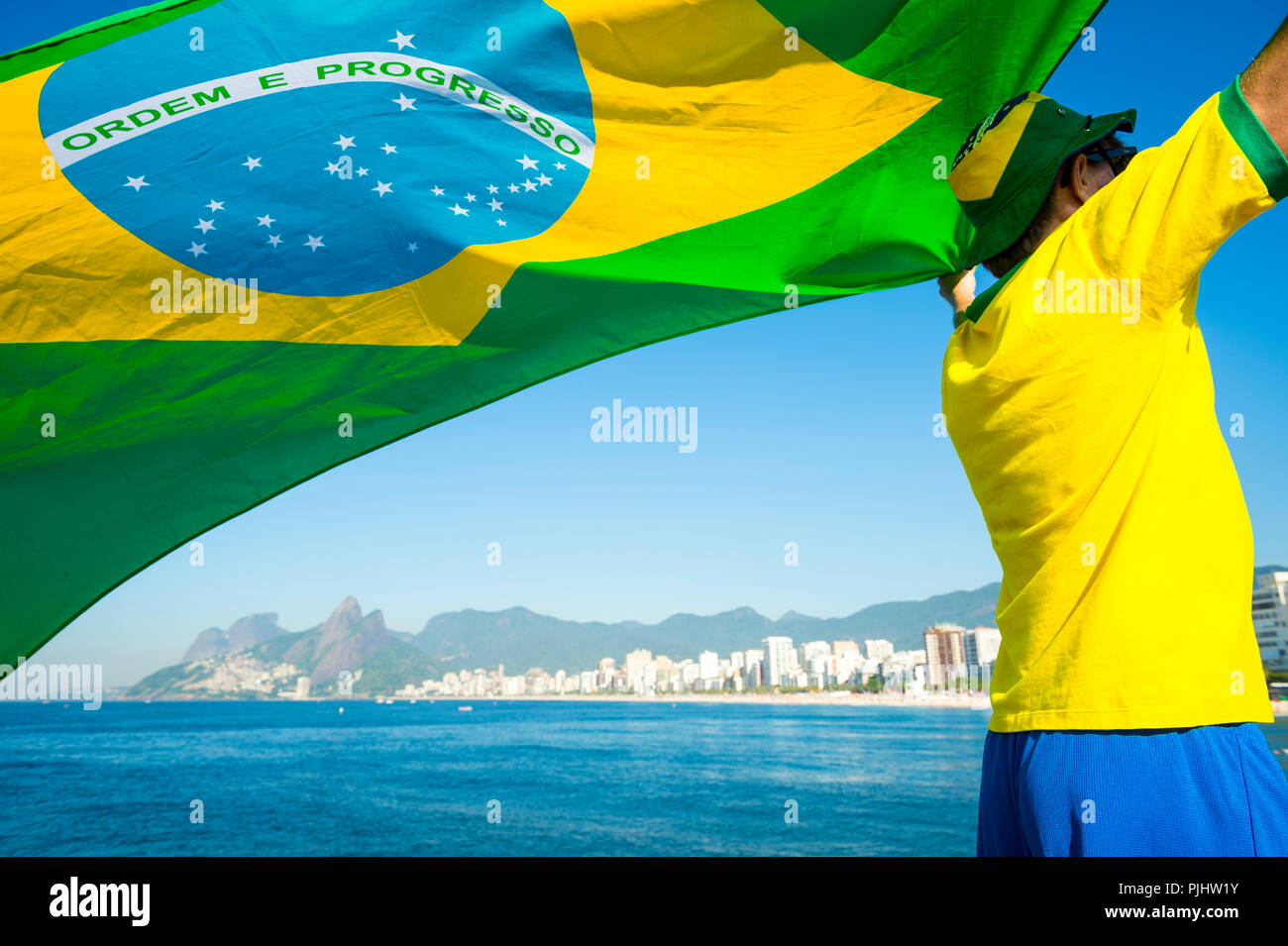 Patriotic Brazilian man flying national flag in front of Ipanema Beach ...