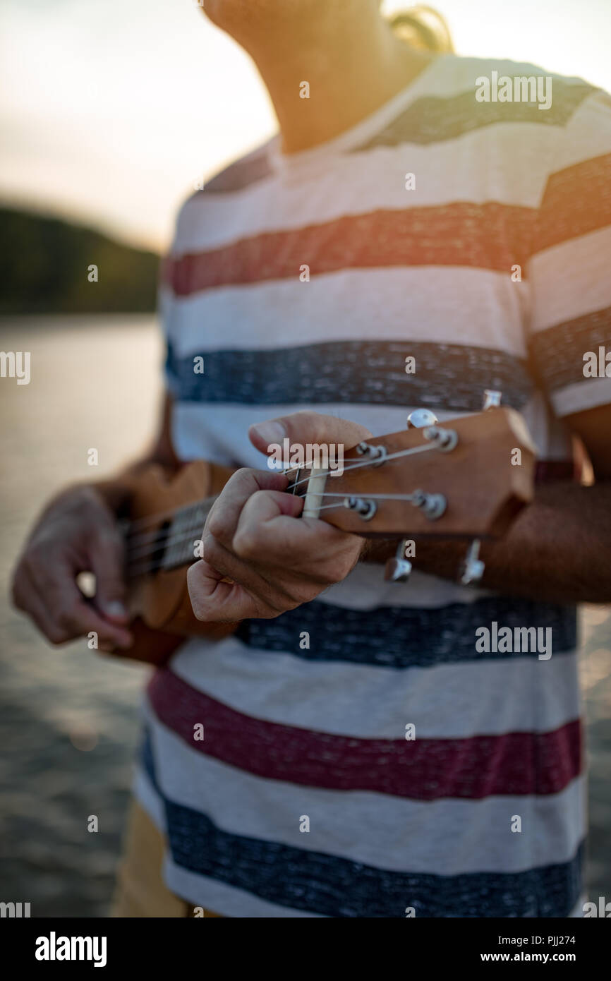 Ukulele in the hands of a young musician. Sunset over water Stock Photo ...