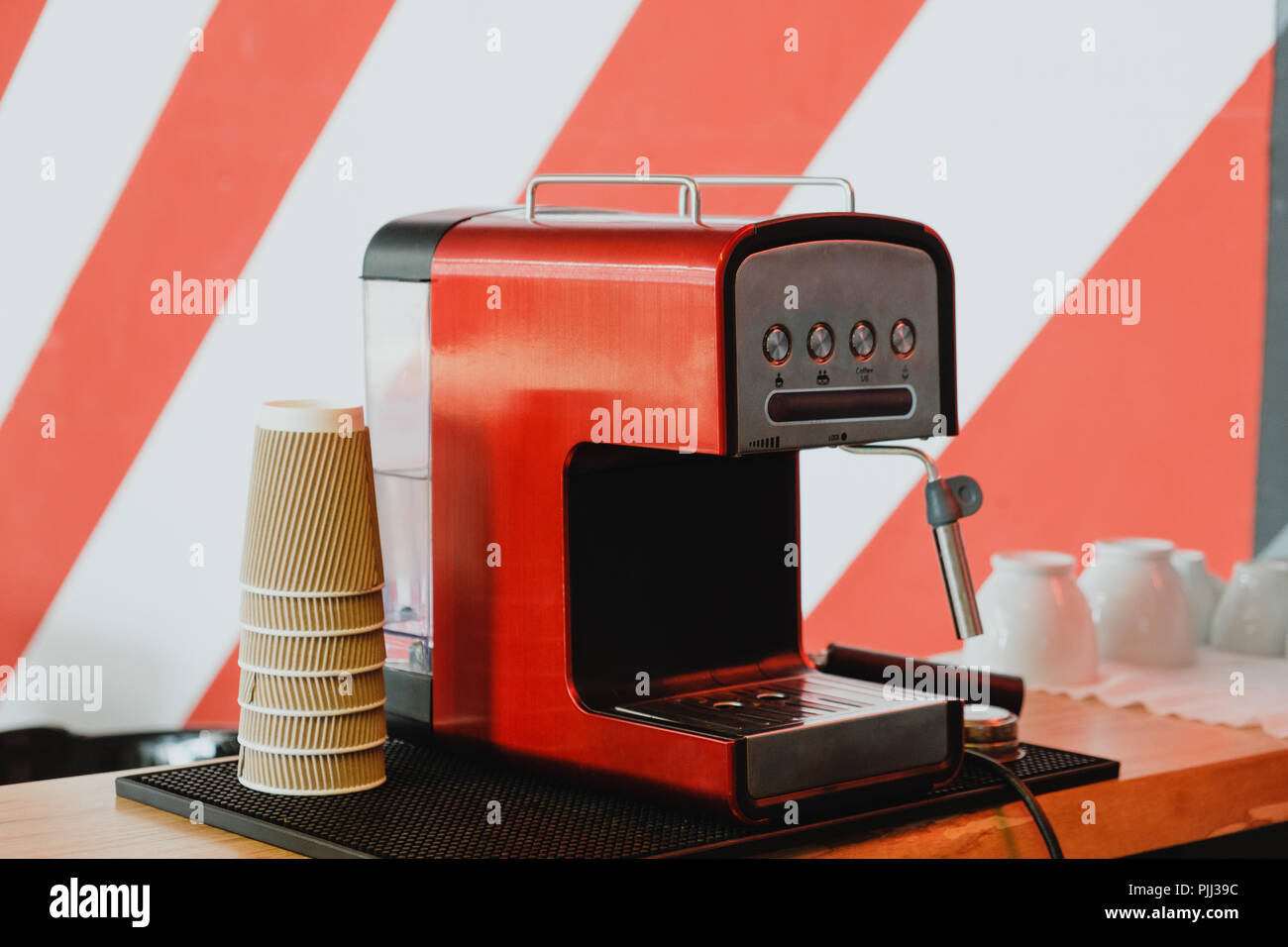 A nice shiny red coffee machine with paper and ceramic cups on a stripy ...