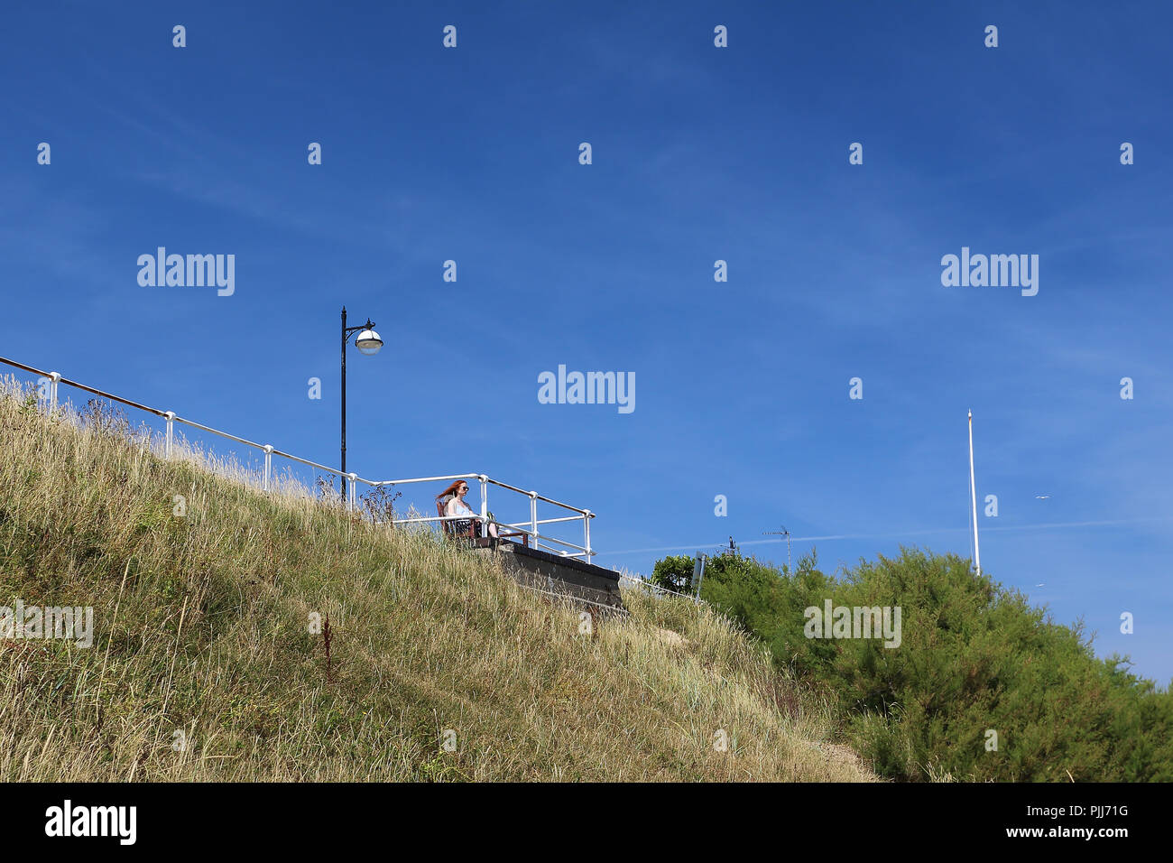 A woman sits atop a cliff overlooking the beach at Southwold, Suffolk ...