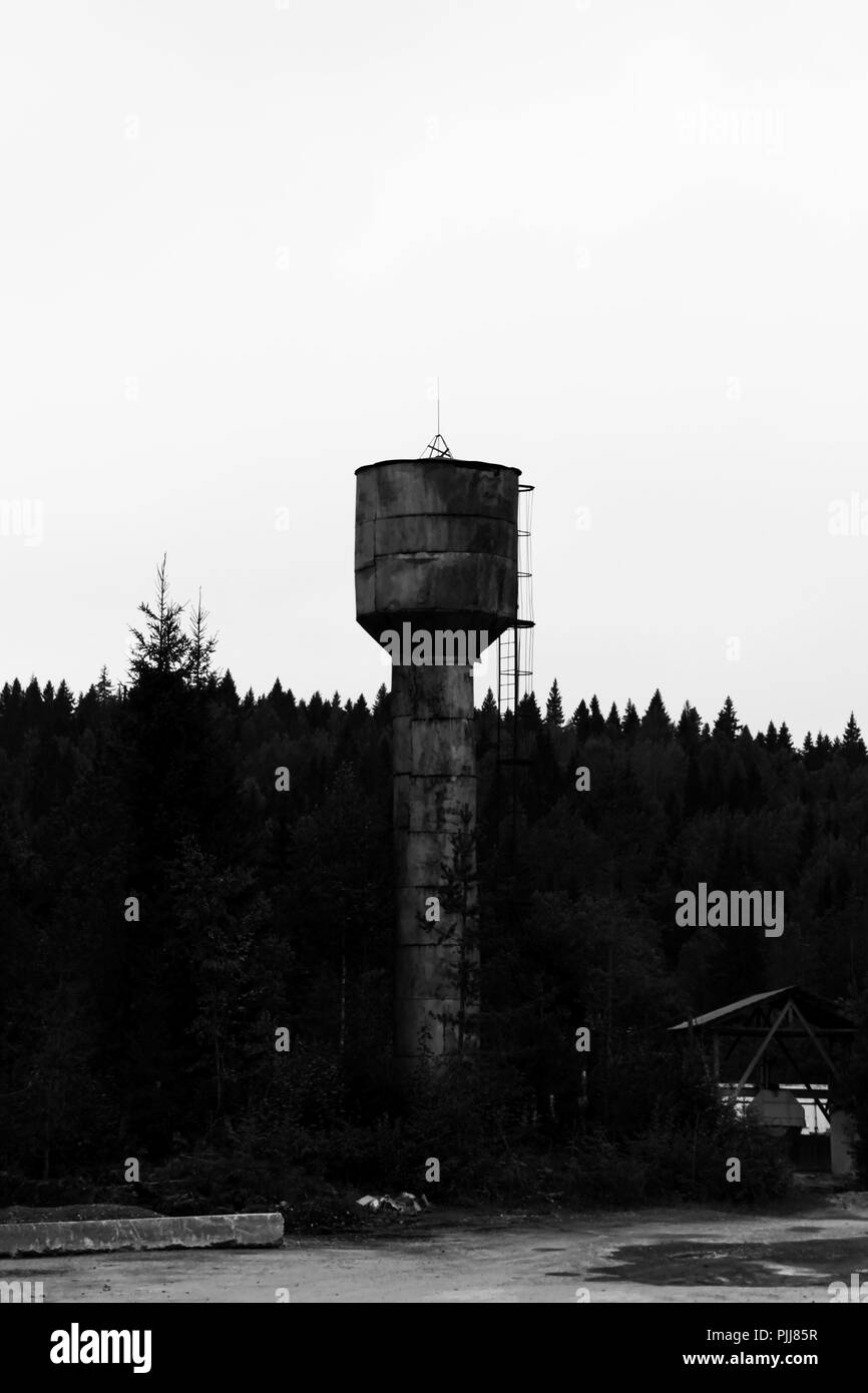 The old rusty water tower with a staircase stands near the forest ...