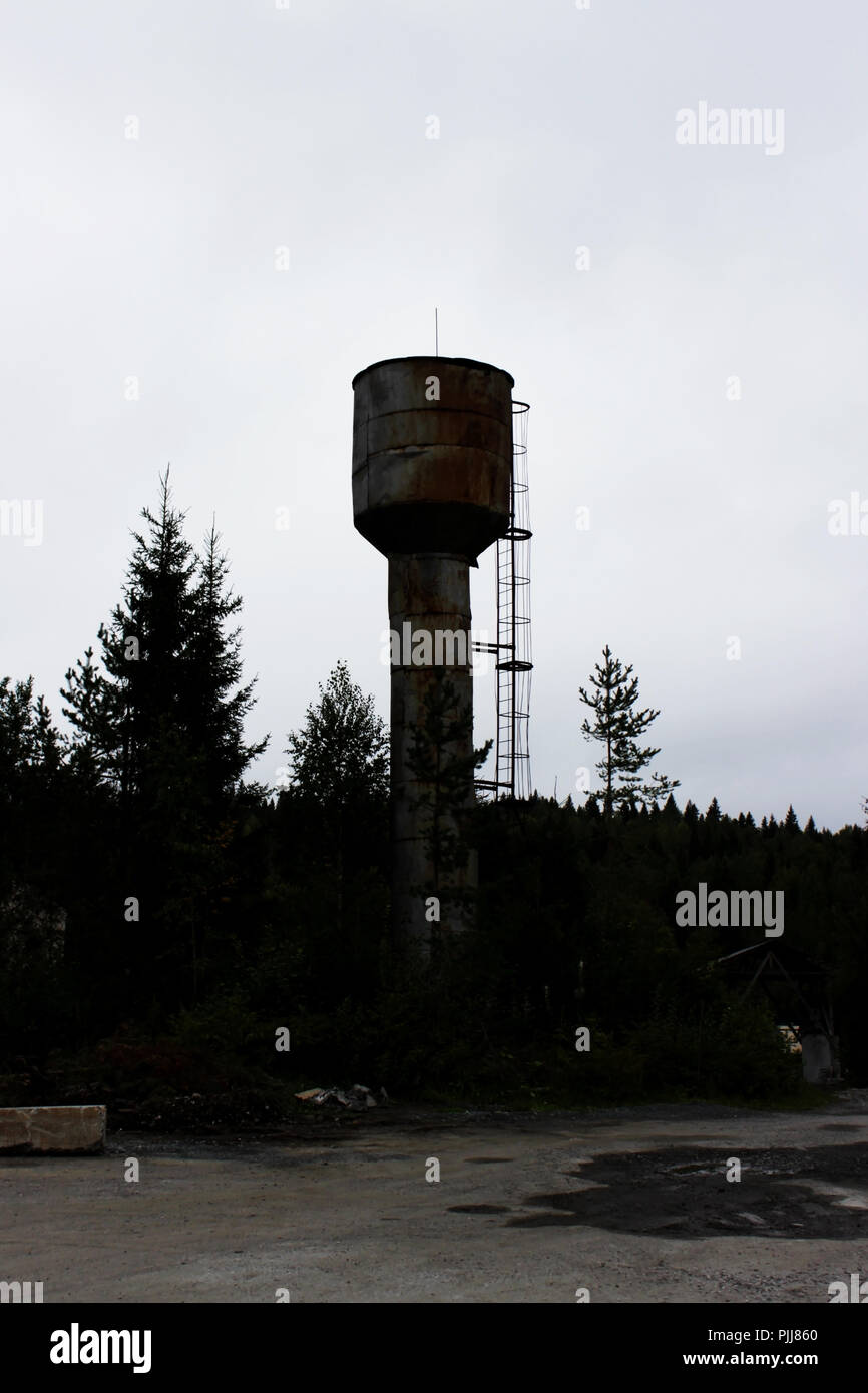 The old rusty water tower with a staircase stands near the forest Stock ...